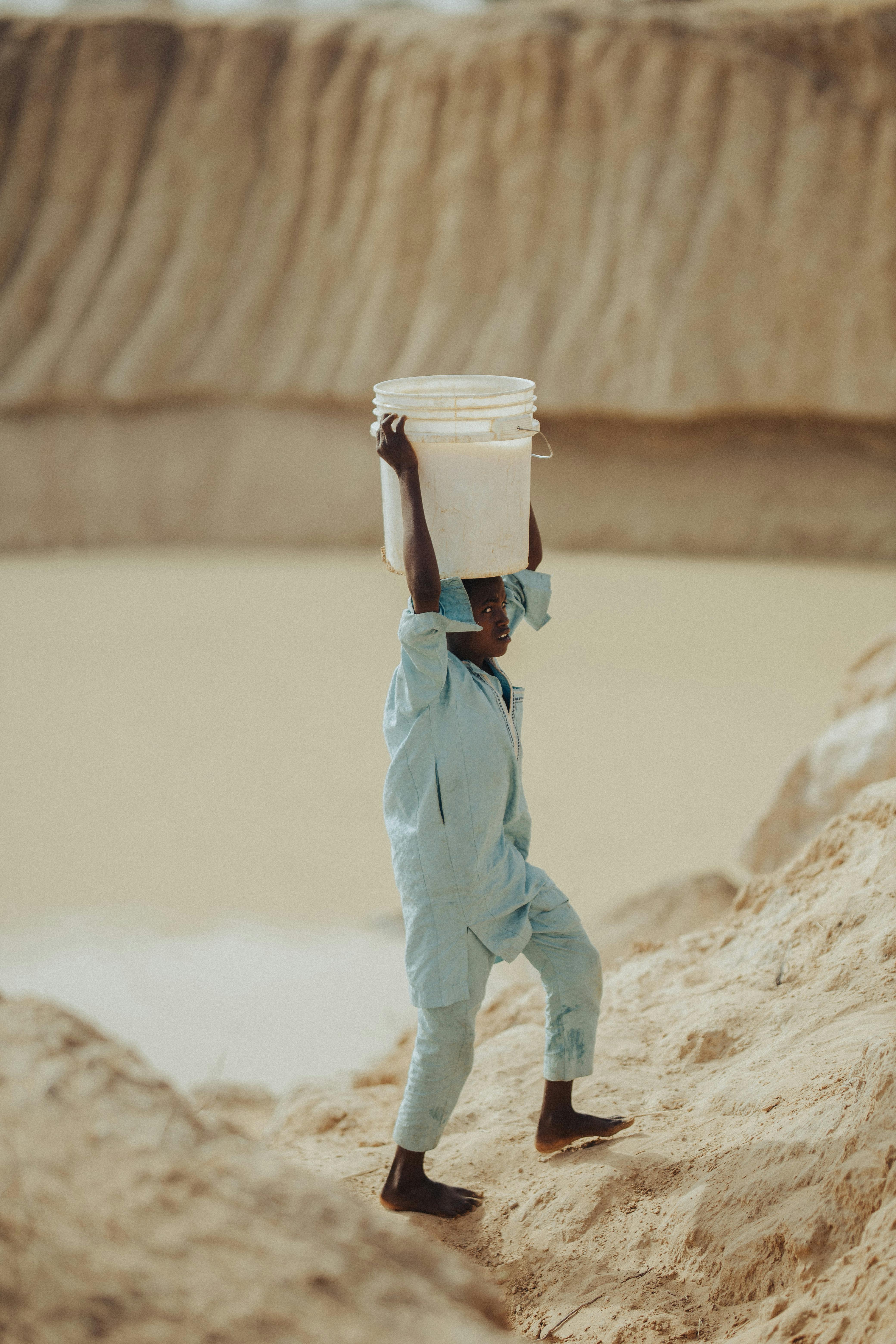 Boy Carrying Bucket on Arid Rocks · Free Stock Photo