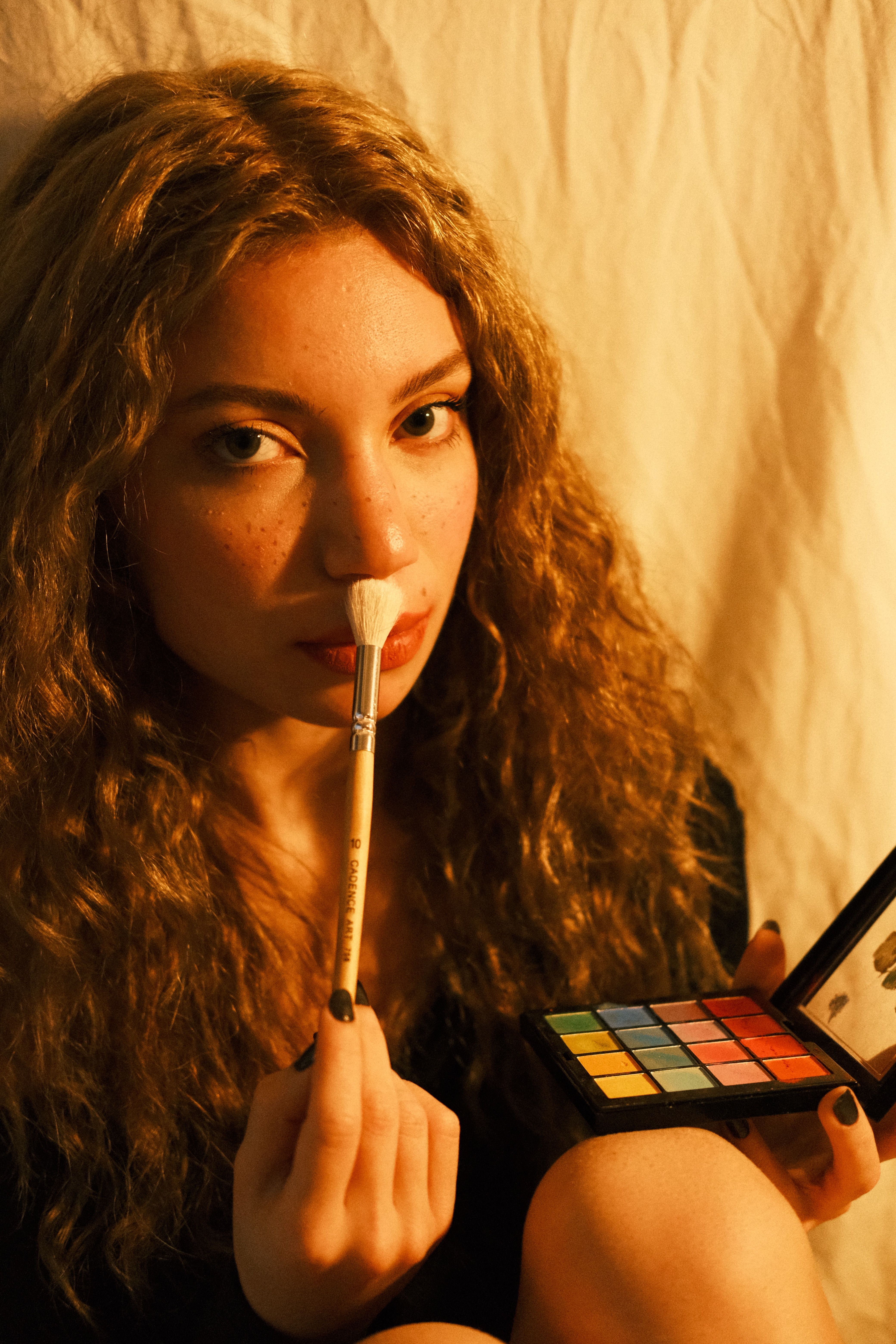 Photo of a Young Woman with Freckles and Curly Hair Holding Eye Shadows ...