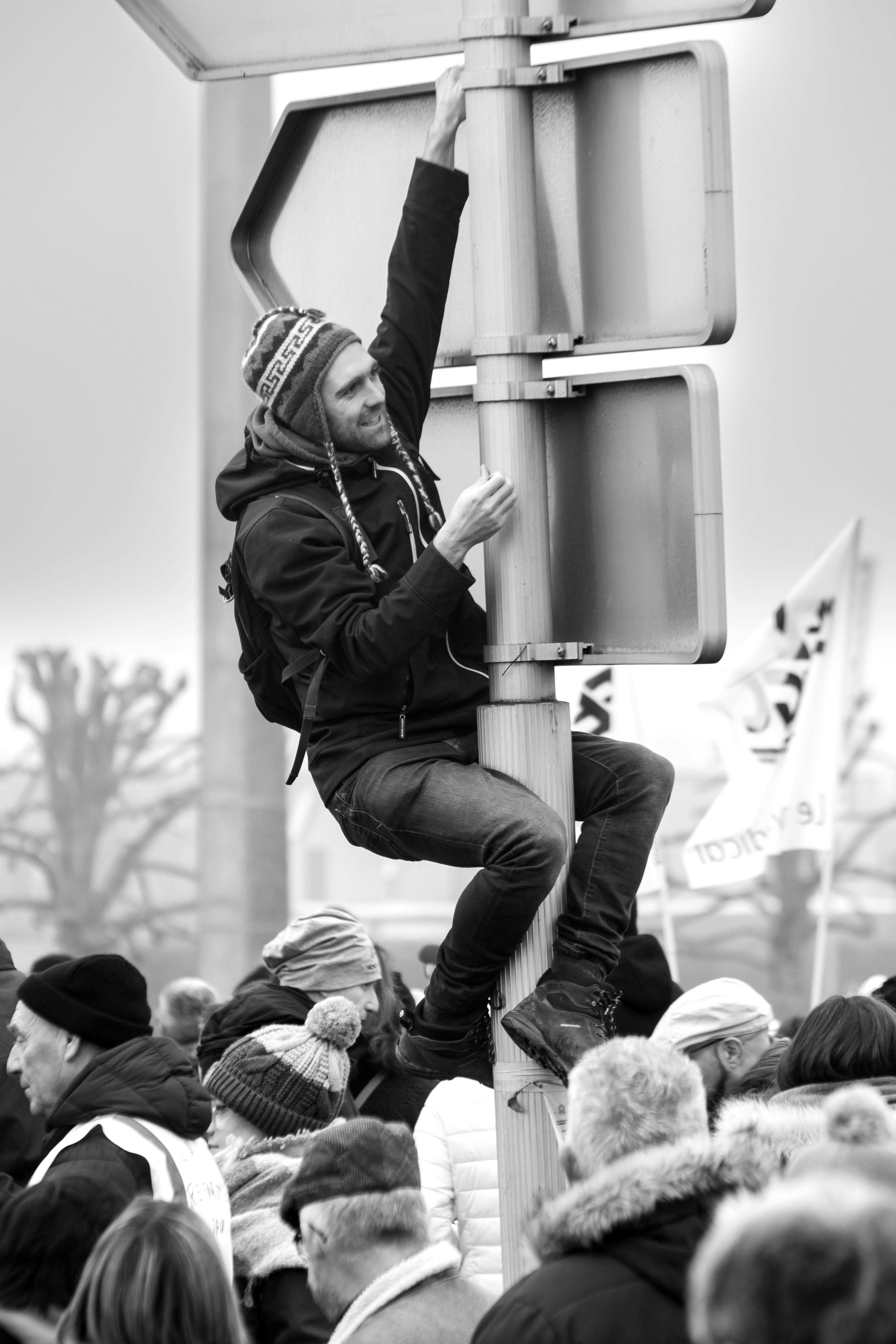 Man Hanging on Road Sign on Gathering · Free Stock Photo
