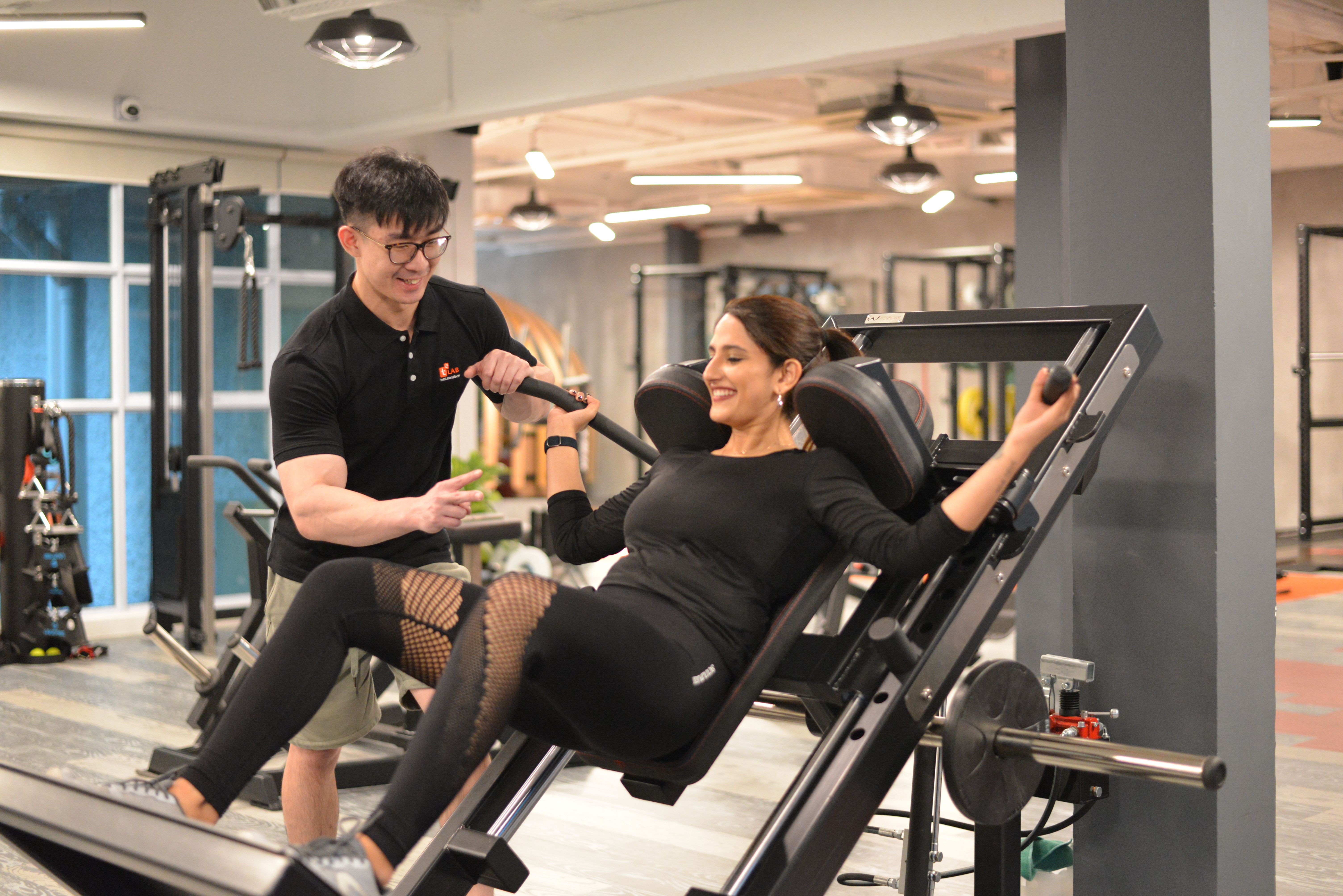 Woman working out with a leg press machine, guided by her Personal ...