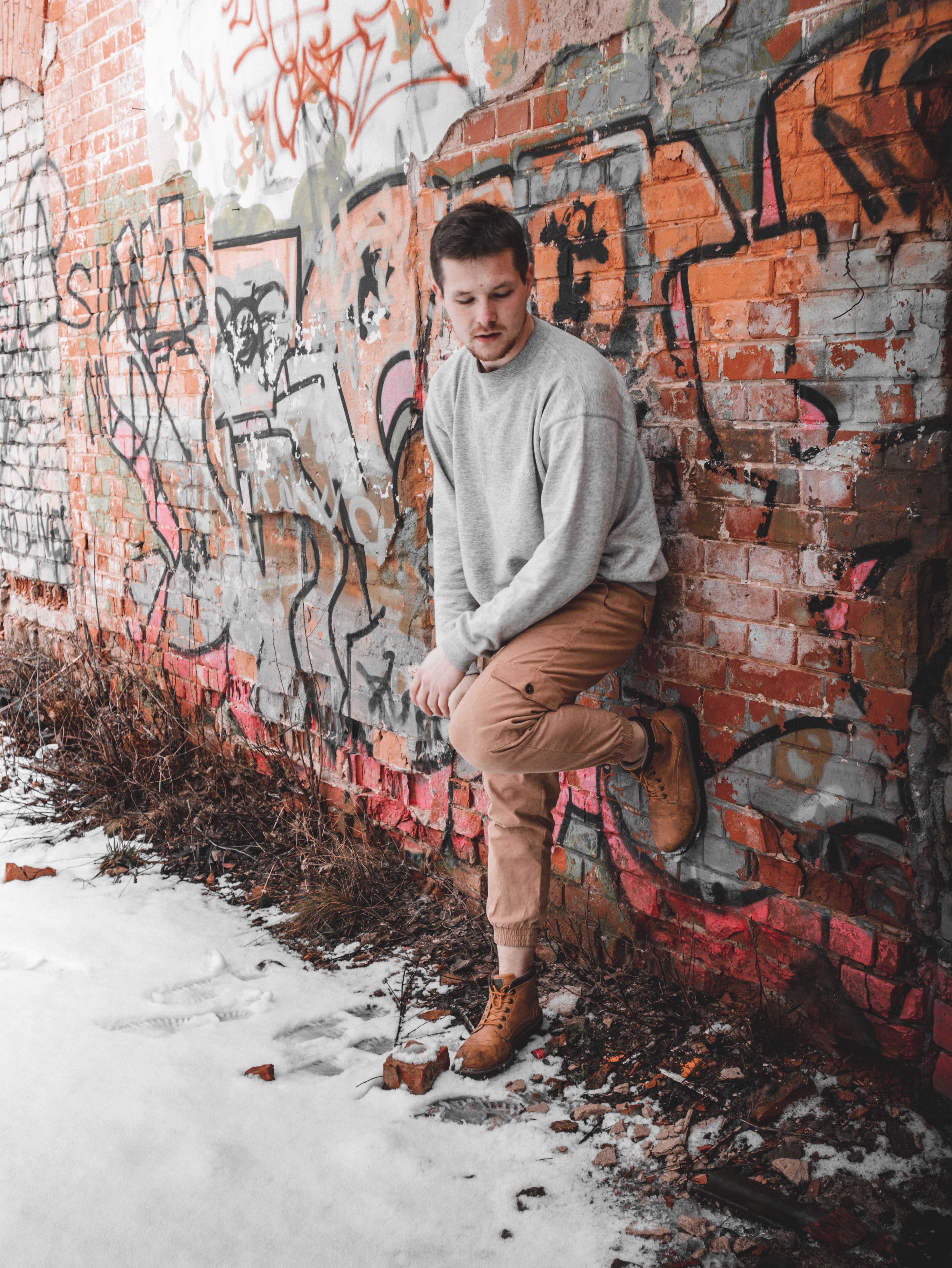 Young Man Leaning on a Brick Wall Covered in Graffiti · Free Stock Photo