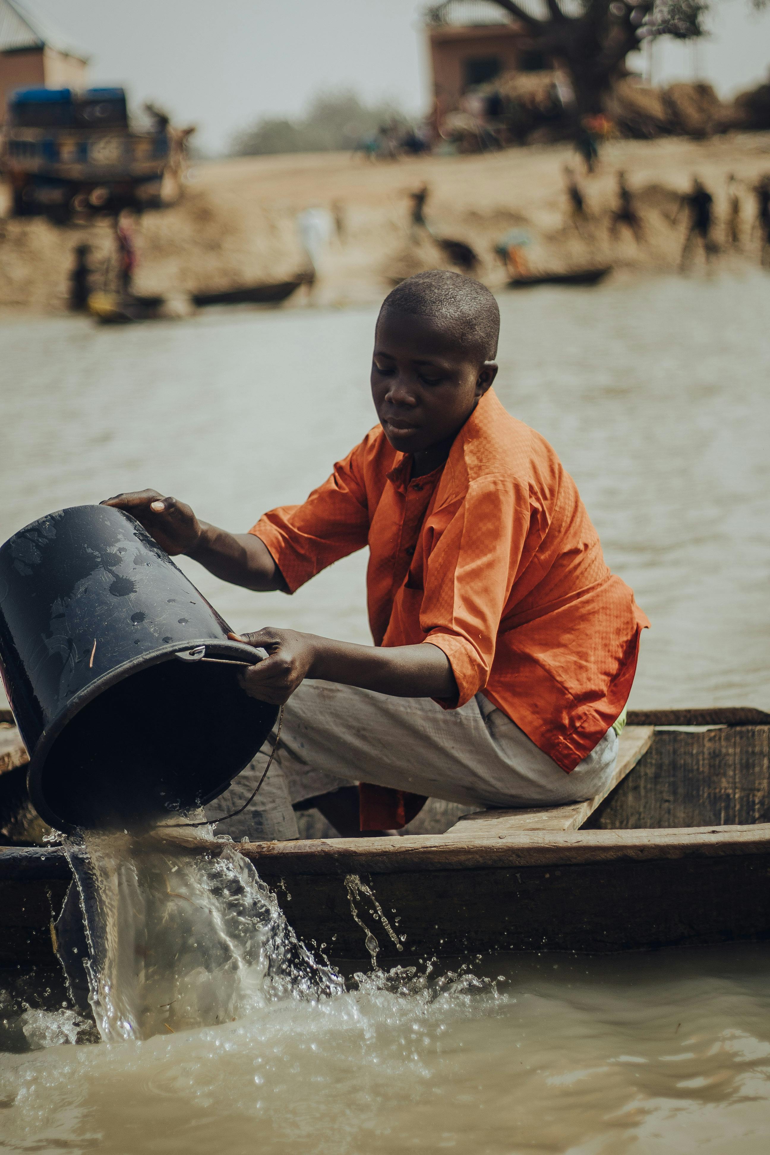 Boy on Canoe Pouring Water Out of Bucket · Free Stock Photo