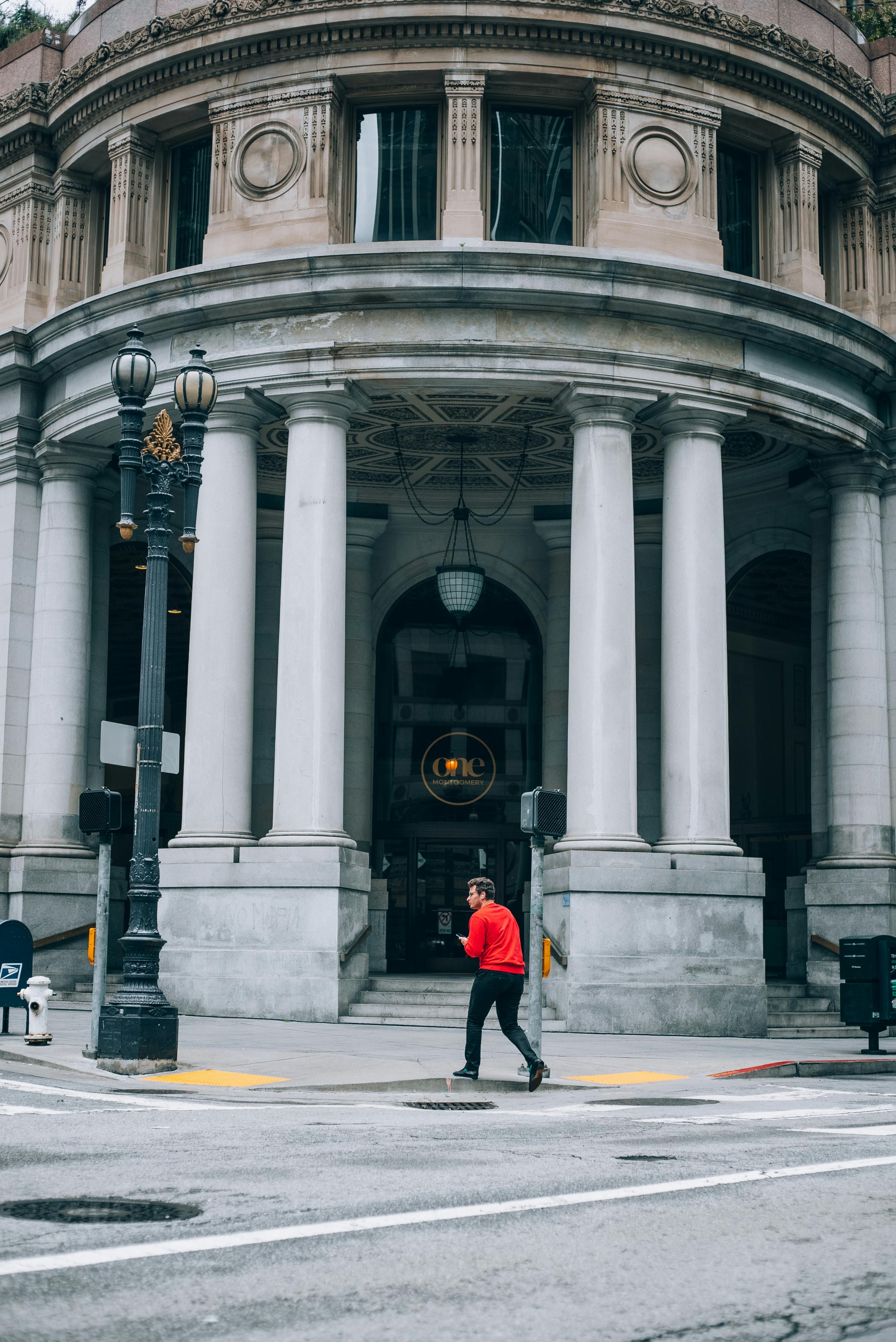 A person walking across the street in front of a large building · Free ...