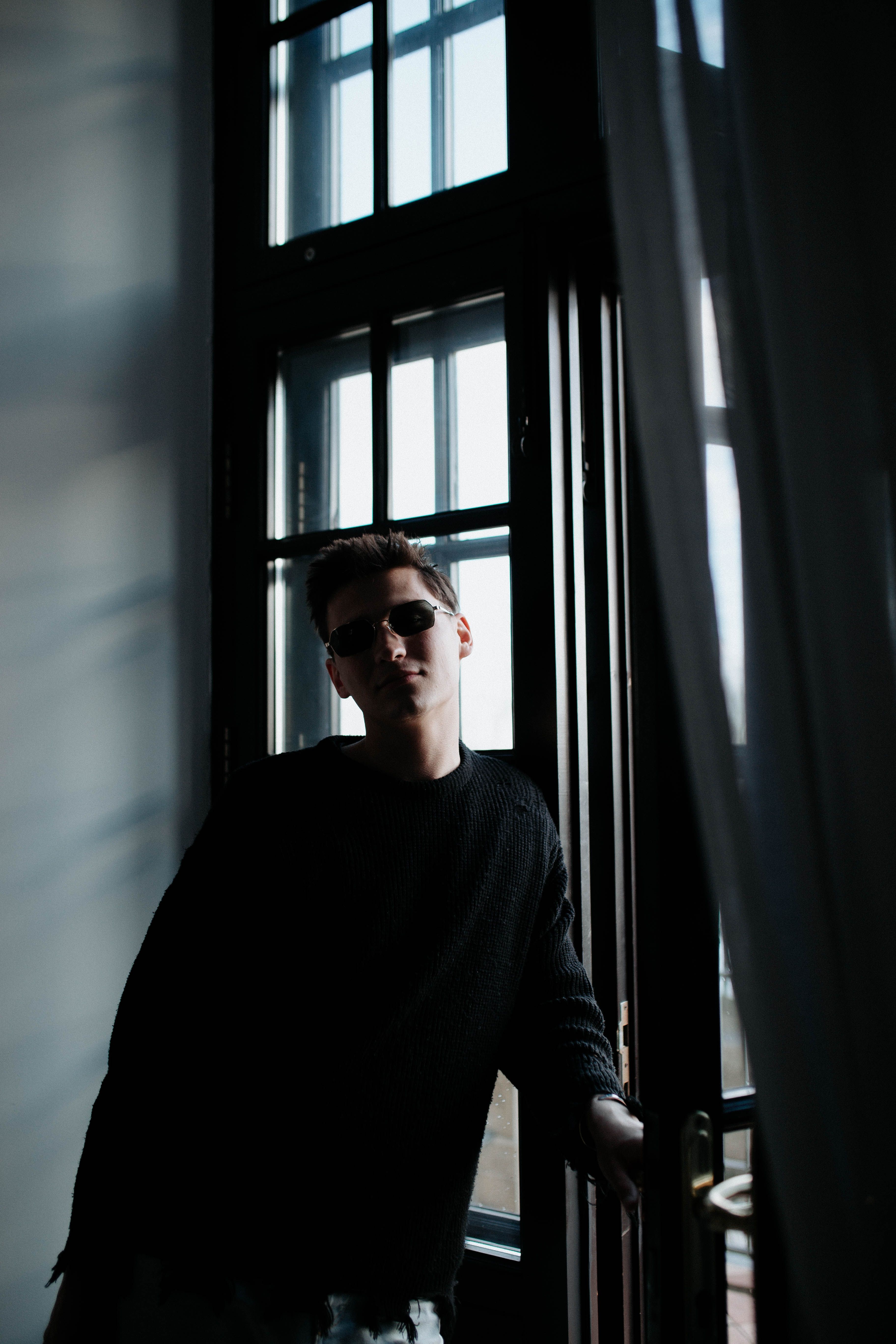 Young Man Wearing Sunglasses Posing against a Window with Curtain ...