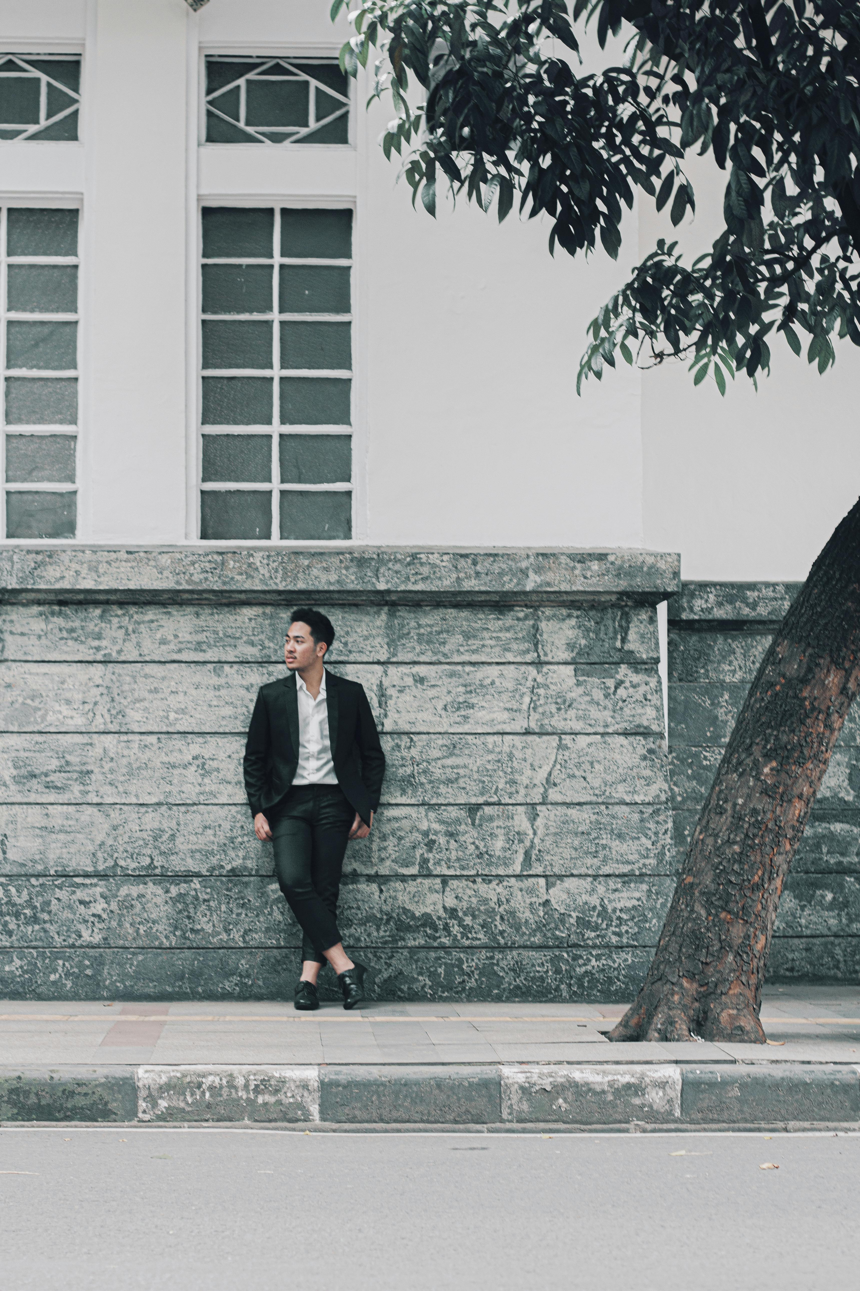 Man in a Black Suit and White Shirt on the Sidewalk Leaning Against a ...