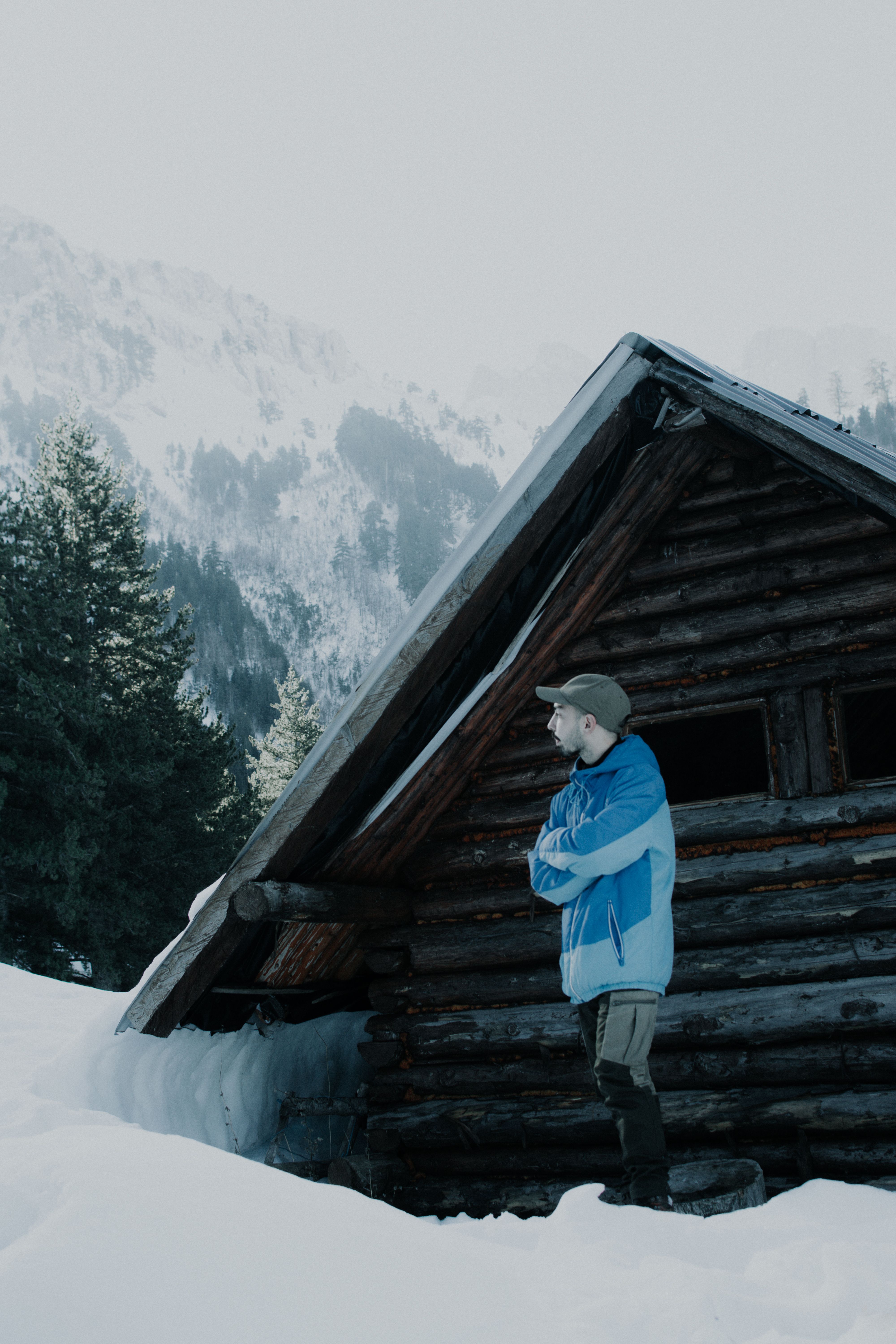 Man in Blue Jacket Standing by Wooden Cabin · Free Stock Photo