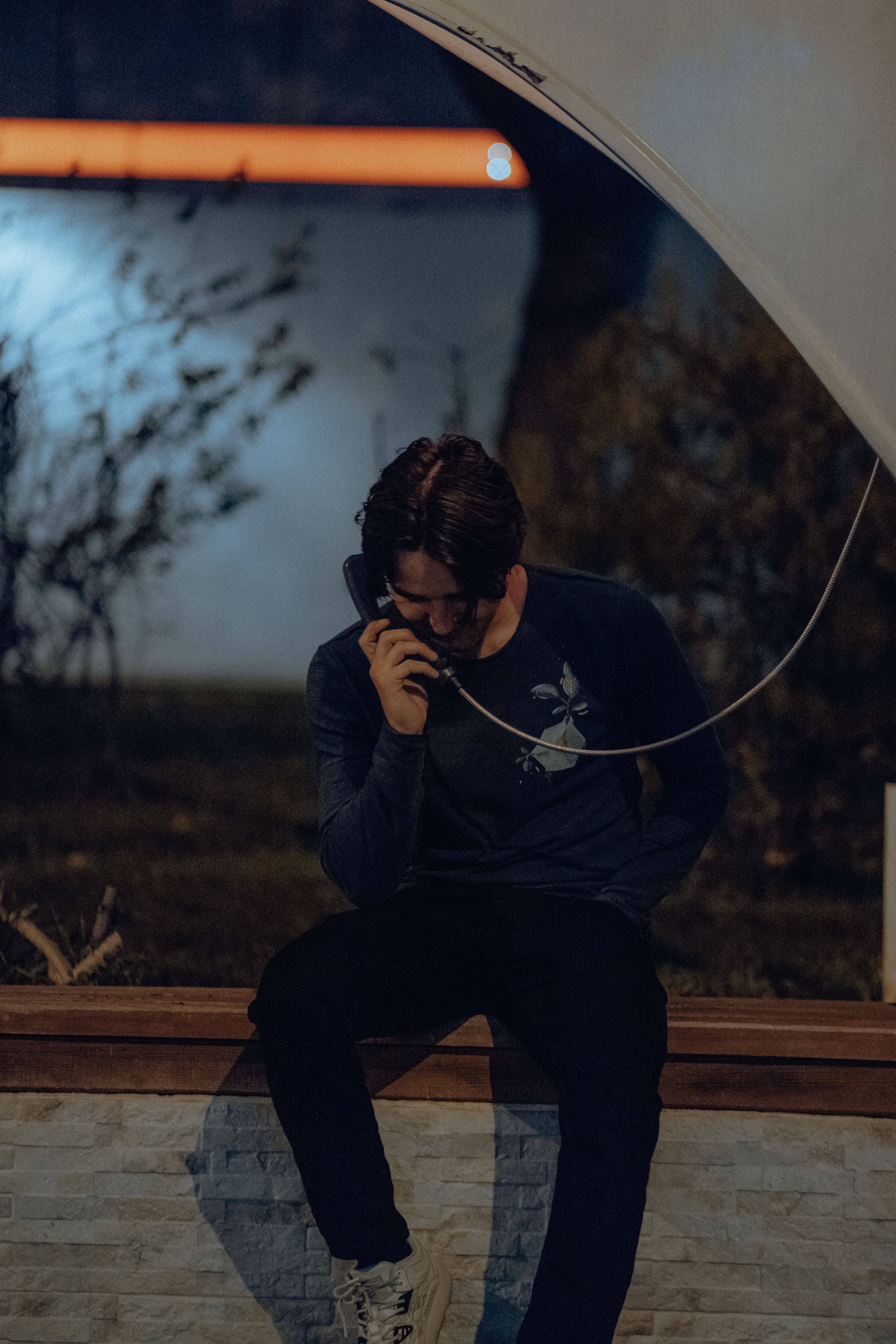 Man Sitting on the Bench and Using a Pay Phone · Free Stock Photo