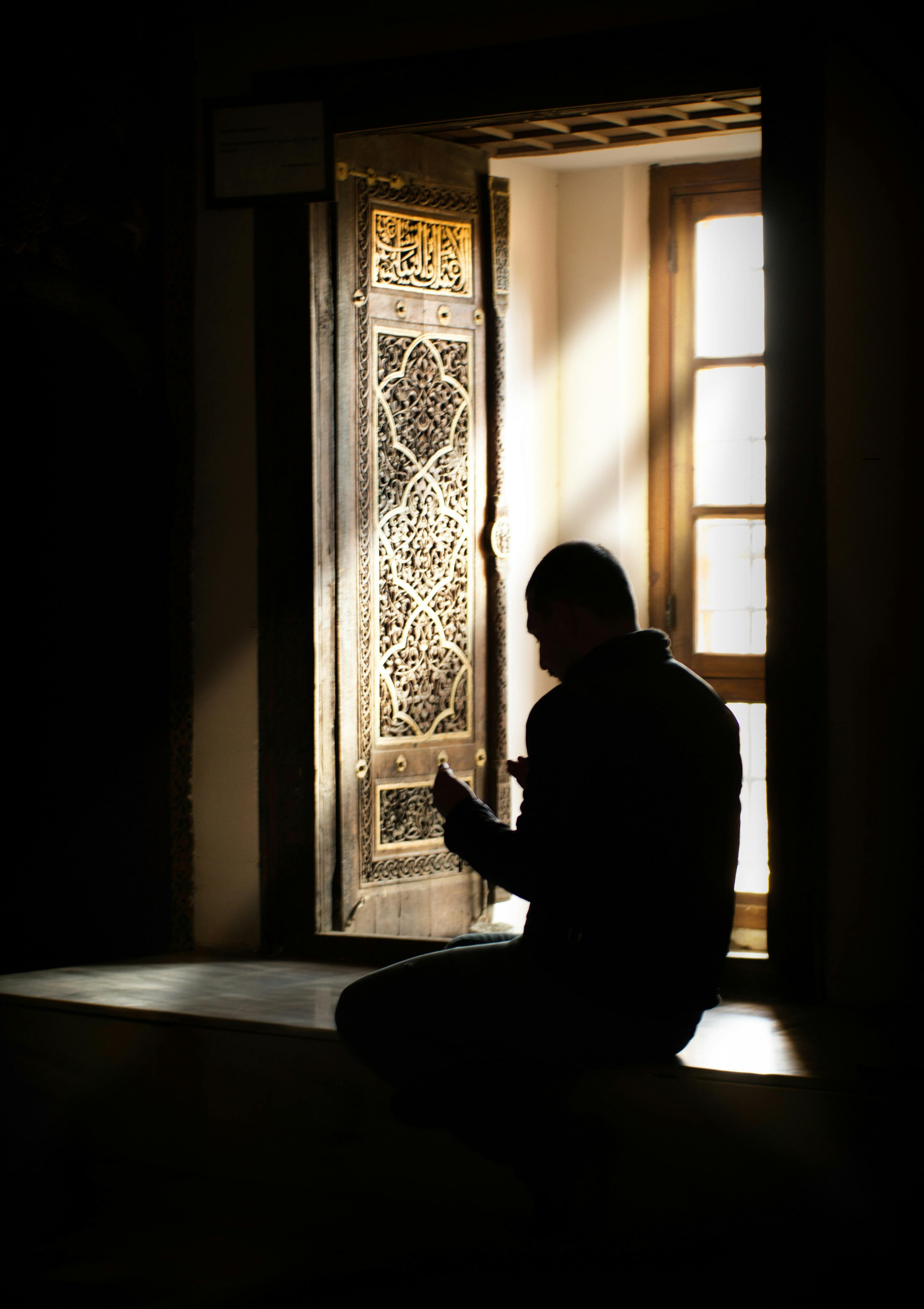 Man Praying by a Window with an Ornamental Shutter · Free Stock Photo