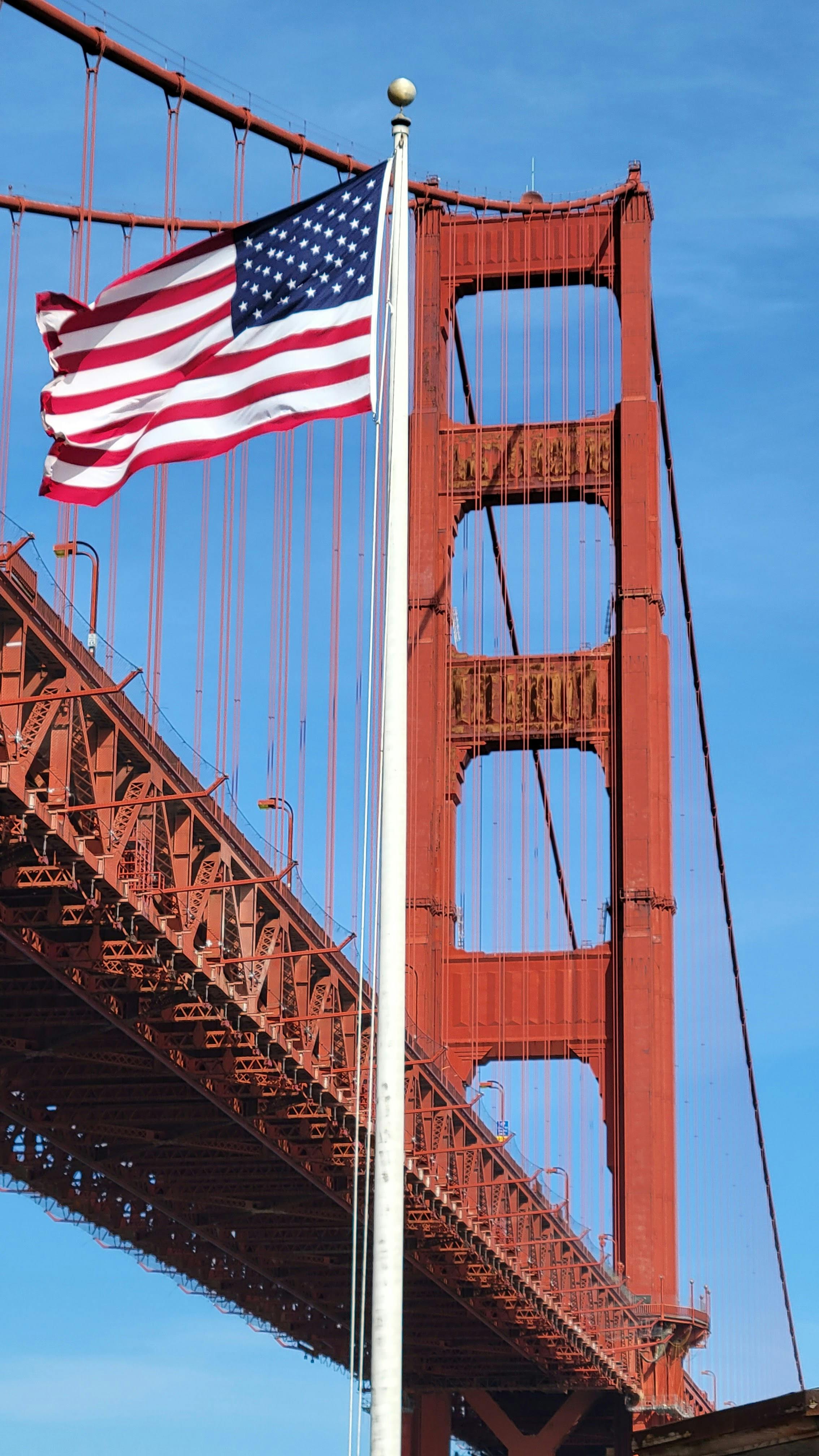 American Flag Against Red Suspension Bridge · Free Stock Photo