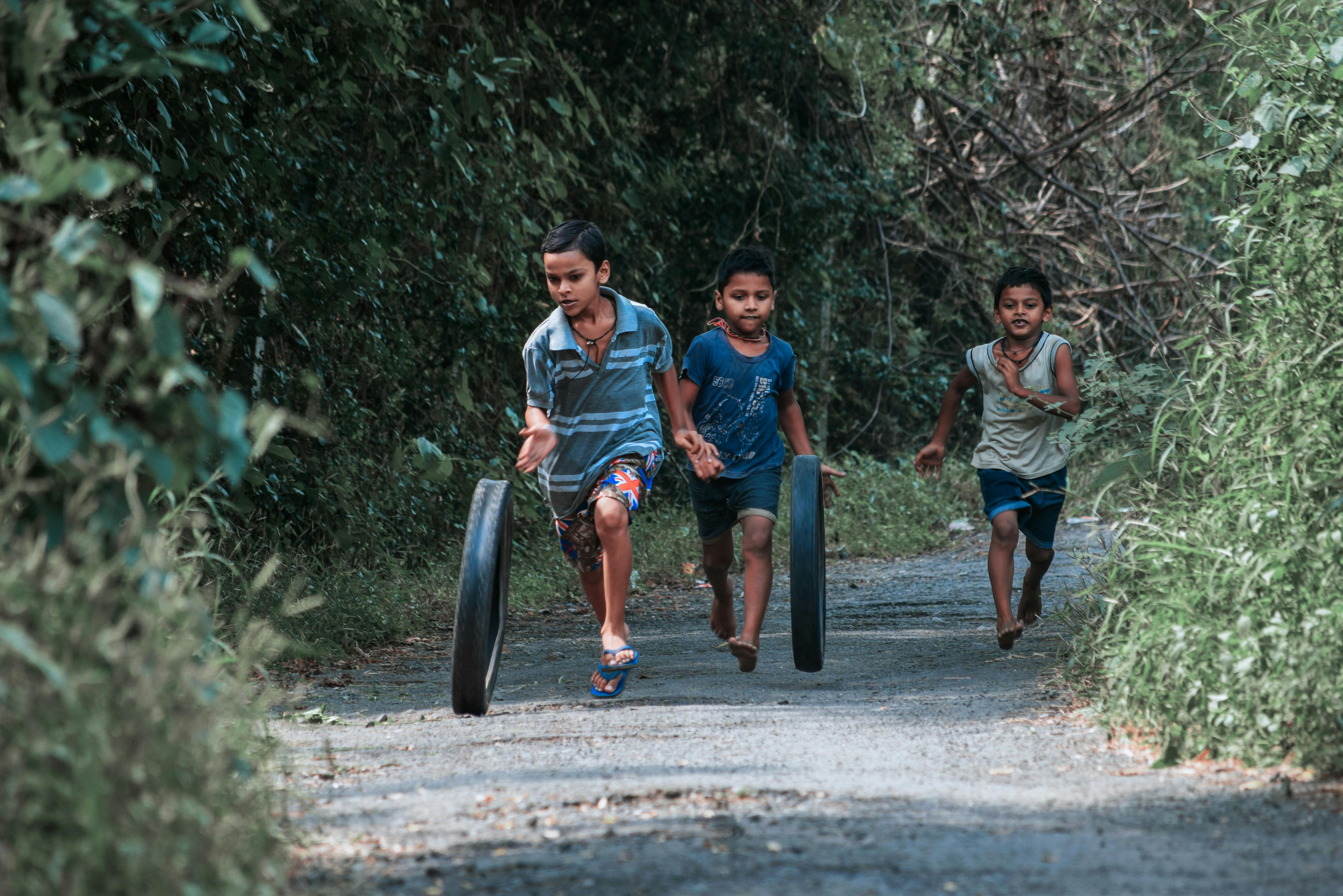 Boys Running and Rolling Tires on Dirt Road in Forest · Free Stock Photo