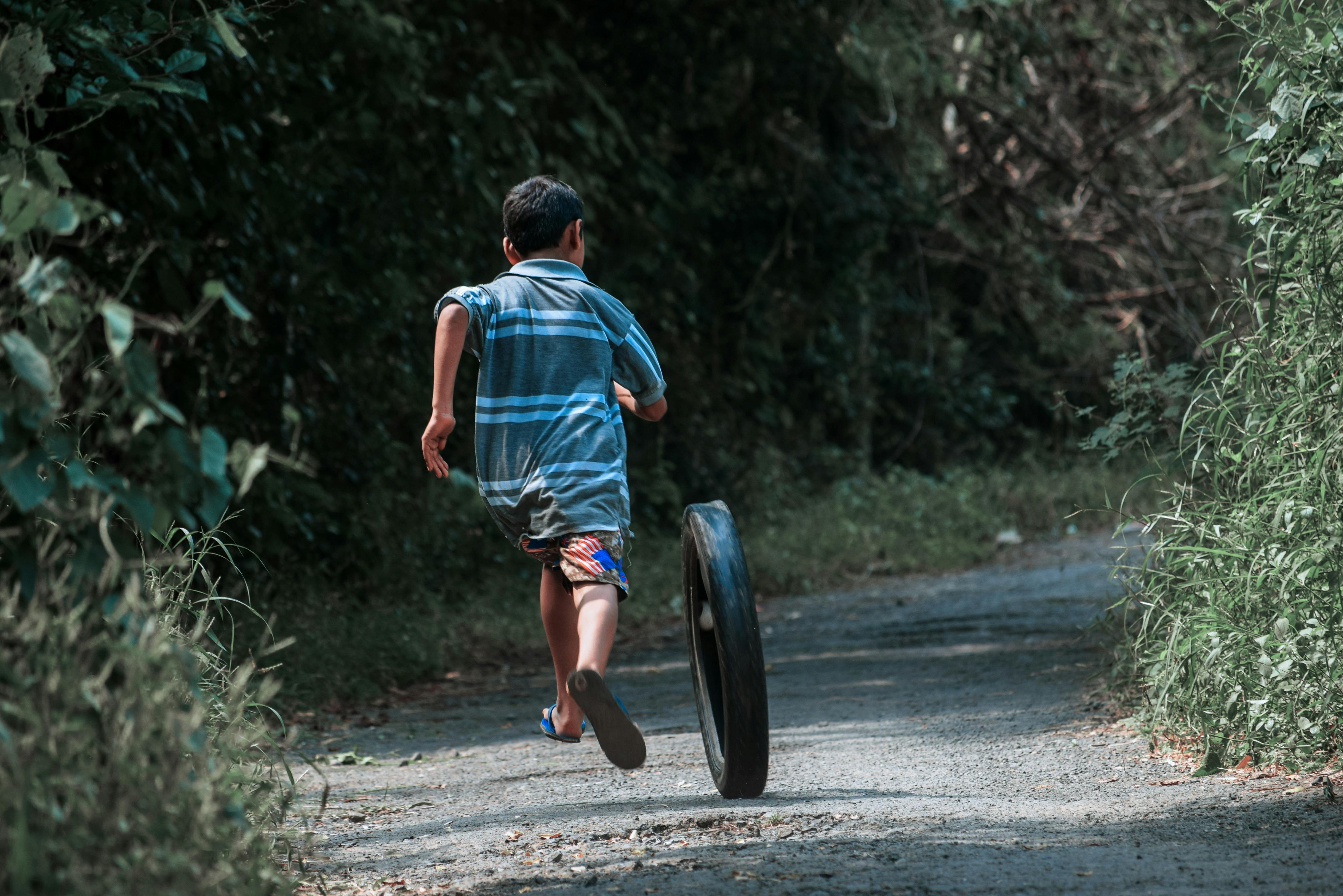 Boy Running Behind Tire on Footpath in Village · Free Stock Photo