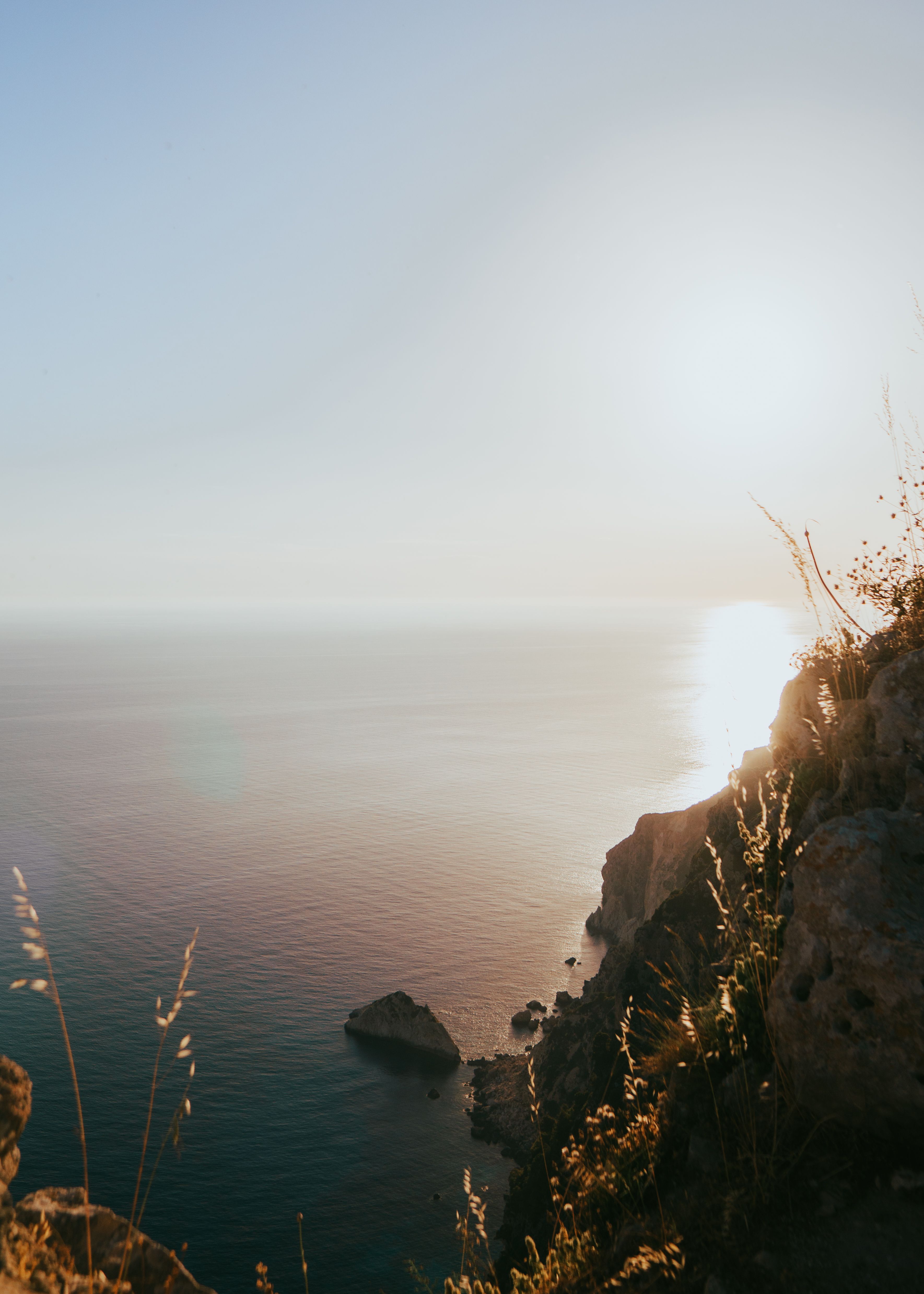 View of a Rocky Cliff and Calm Sea at Sunset · Free Stock Photo