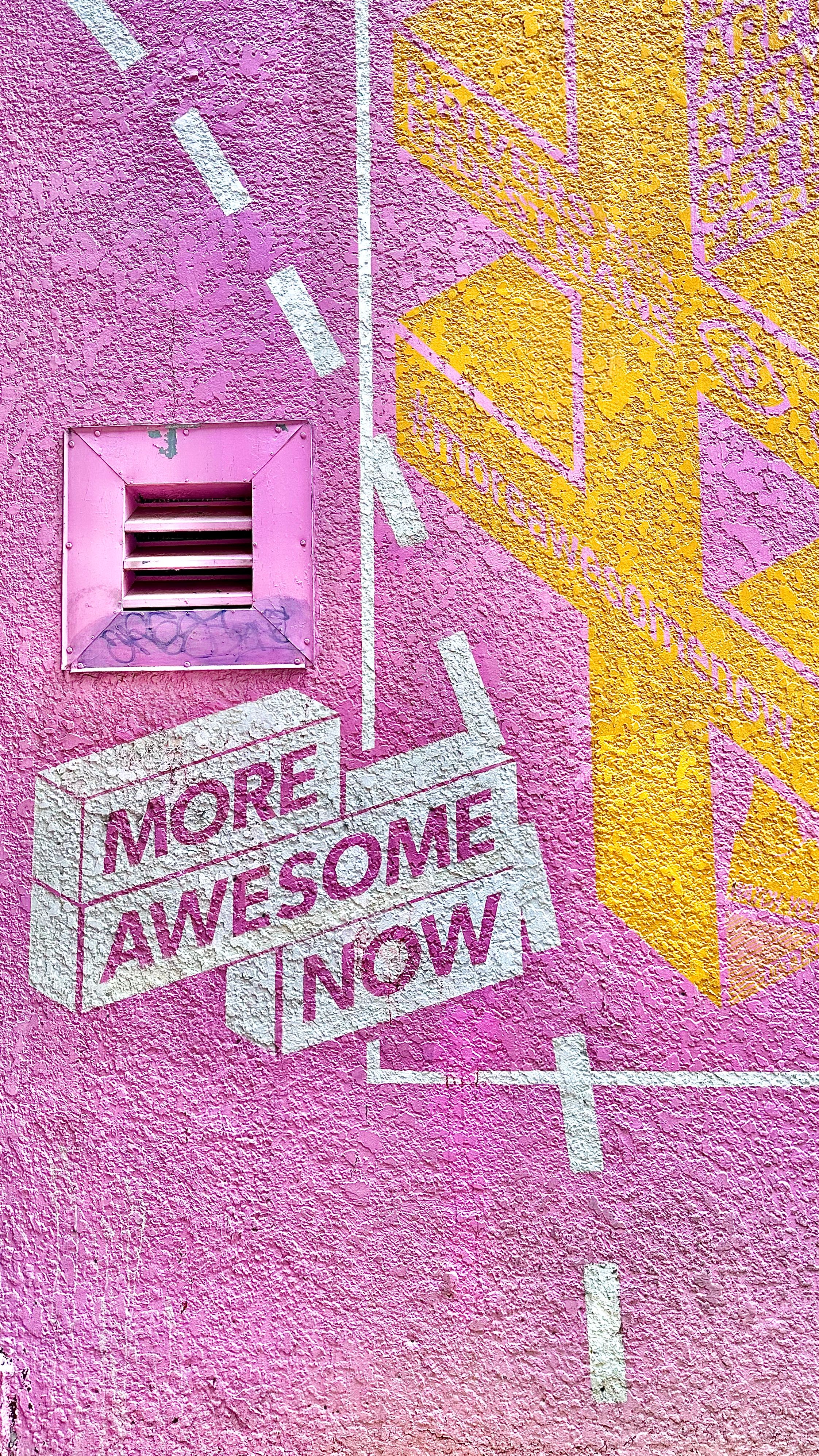 A pink wall with a sign that says more awesome now · Free Stock Photo