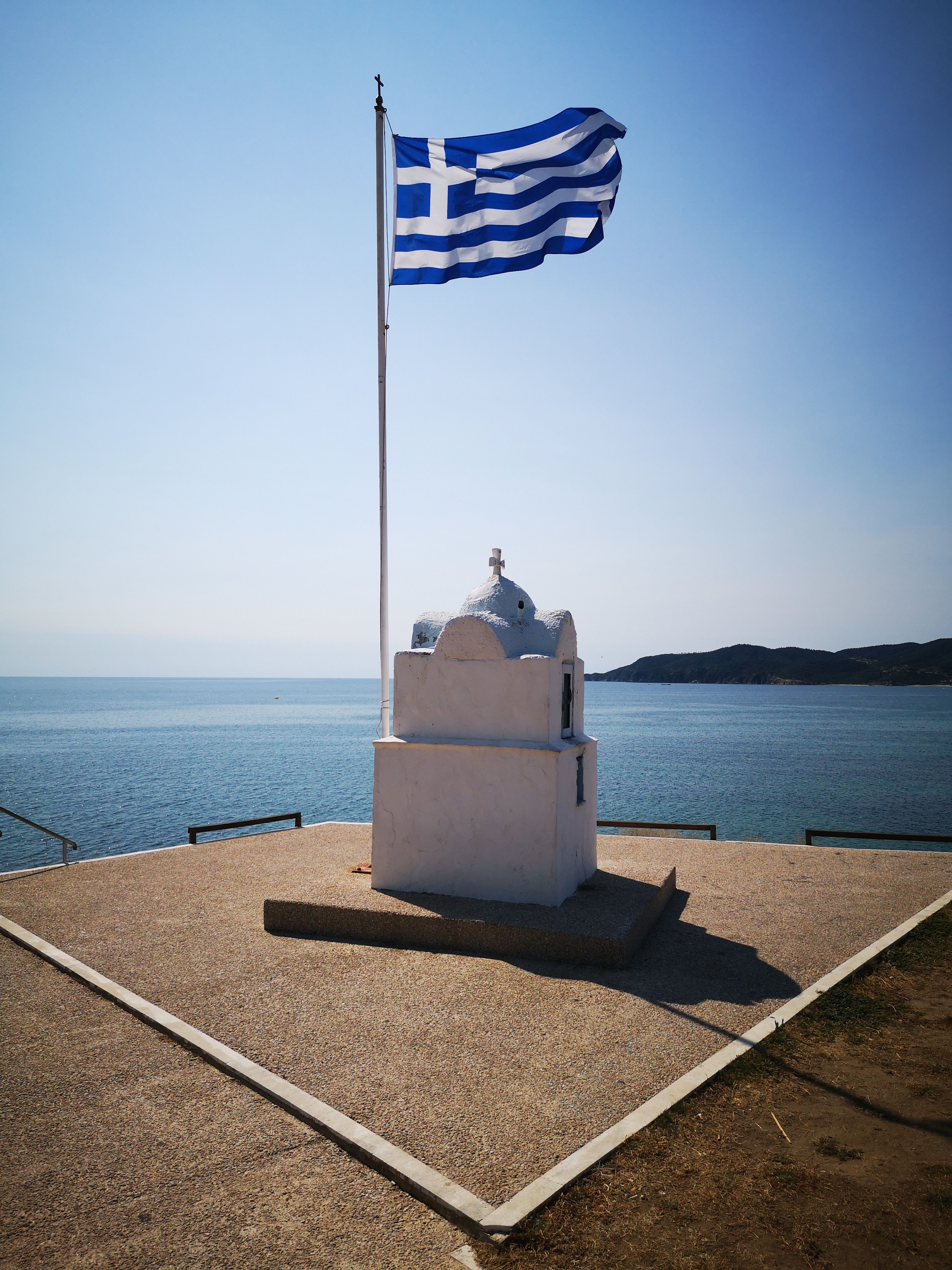 Greek Flag and White Monument on Seashore · Free Stock Photo