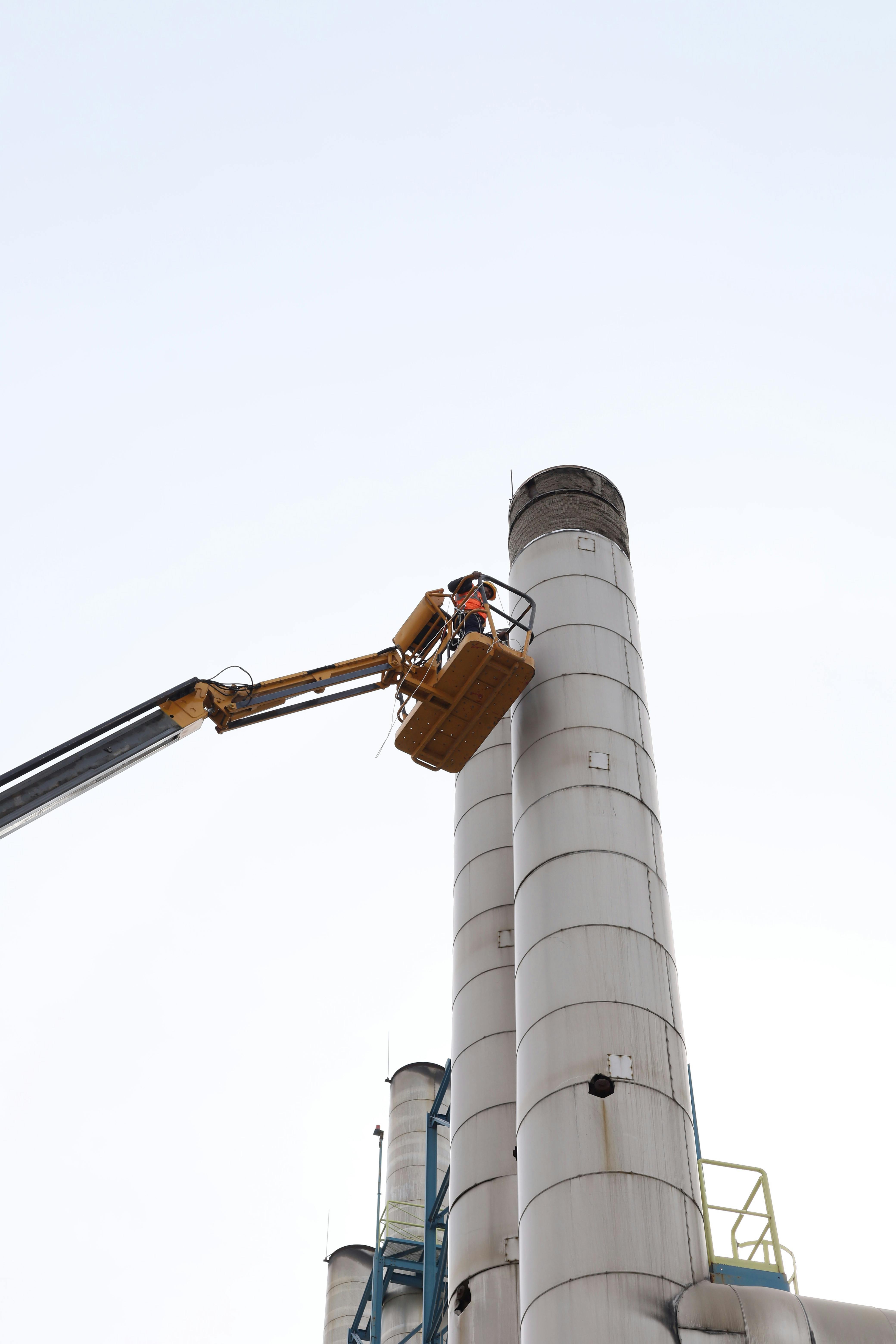 Worker on Jib Crane by Factory Chimneys · Free Stock Photo