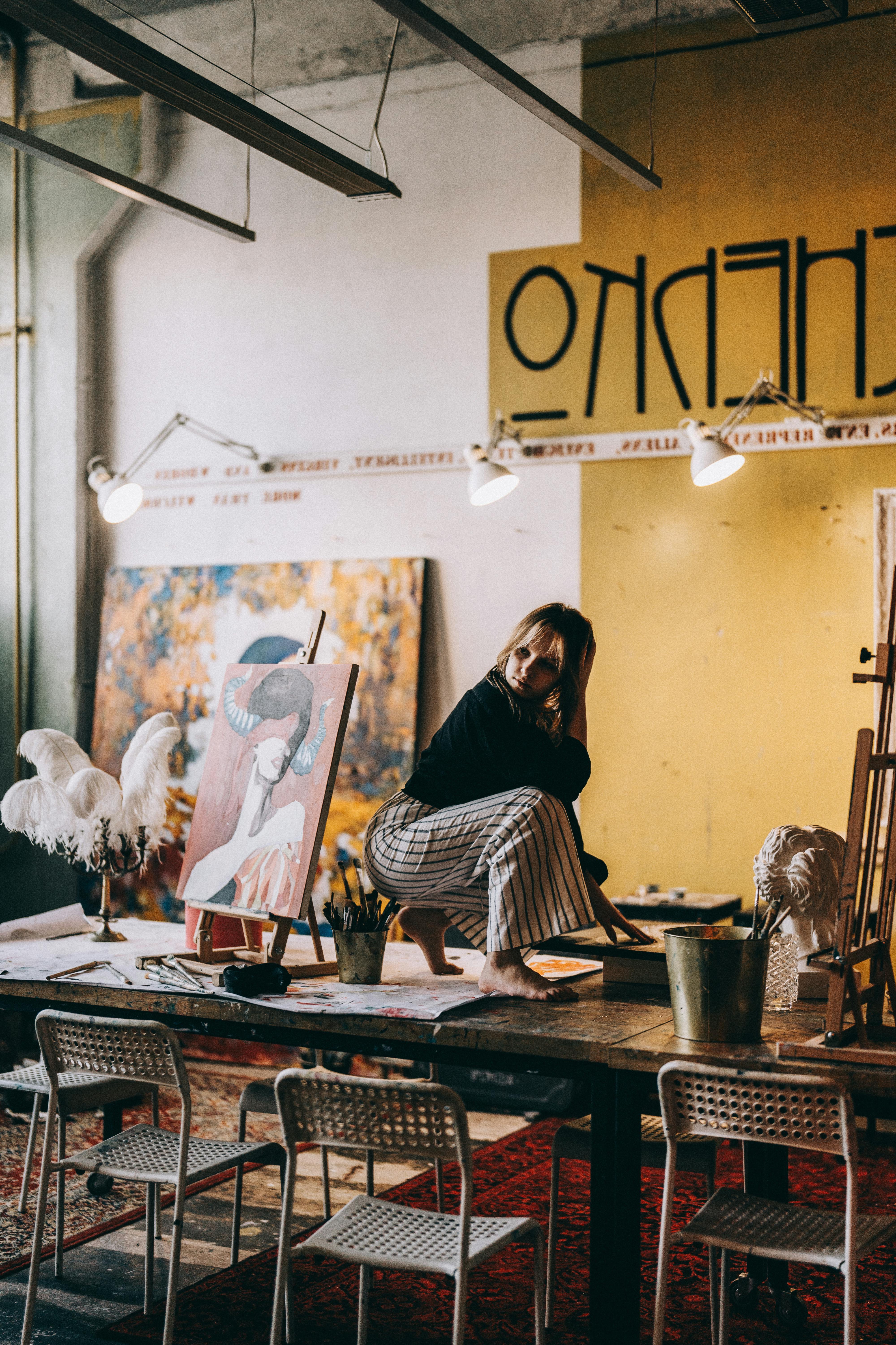 Young Woman Crouching on a Table in an Art Studio · Free Stock Photo