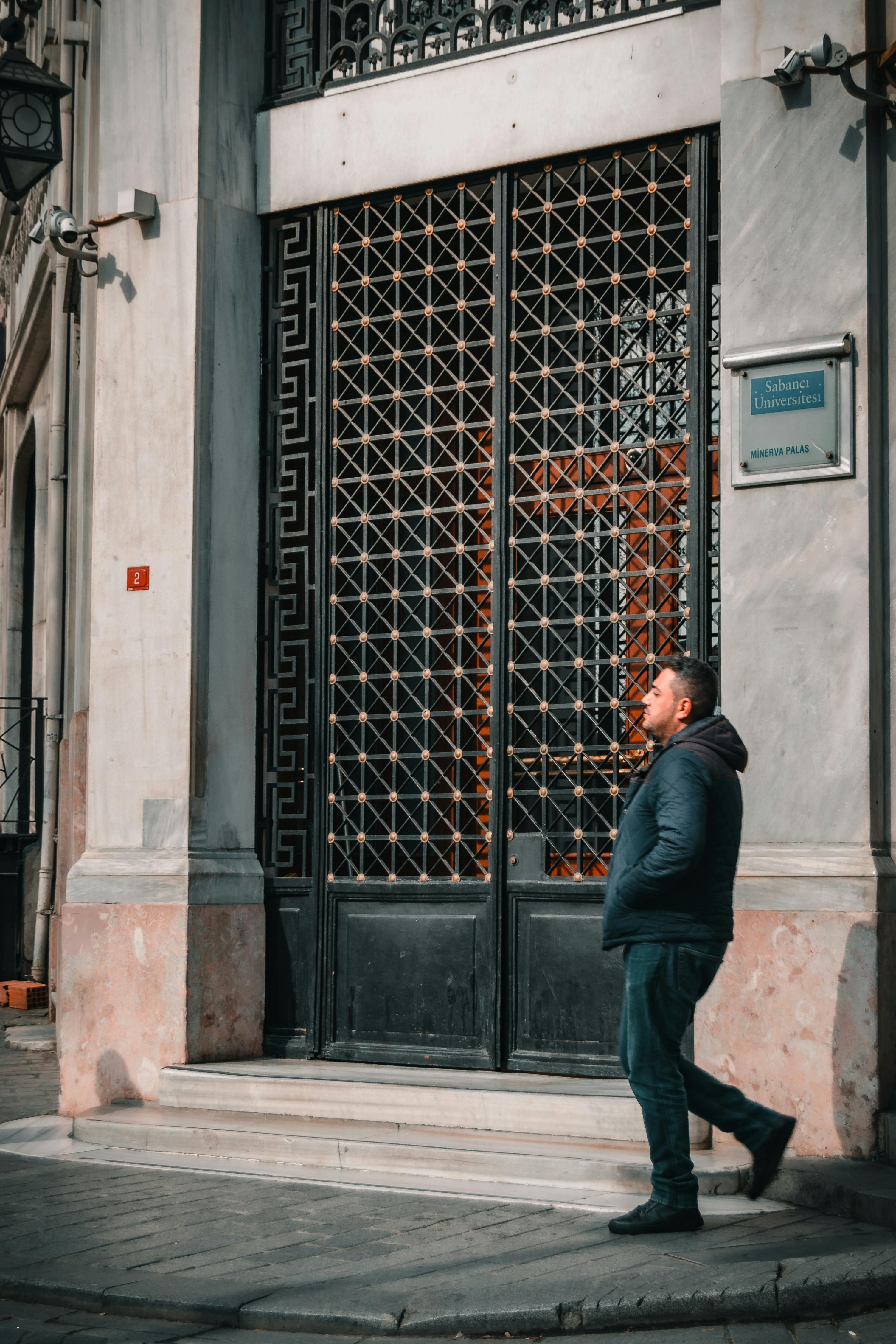 Man Walking Past a Closed University Gate · Free Stock Photo