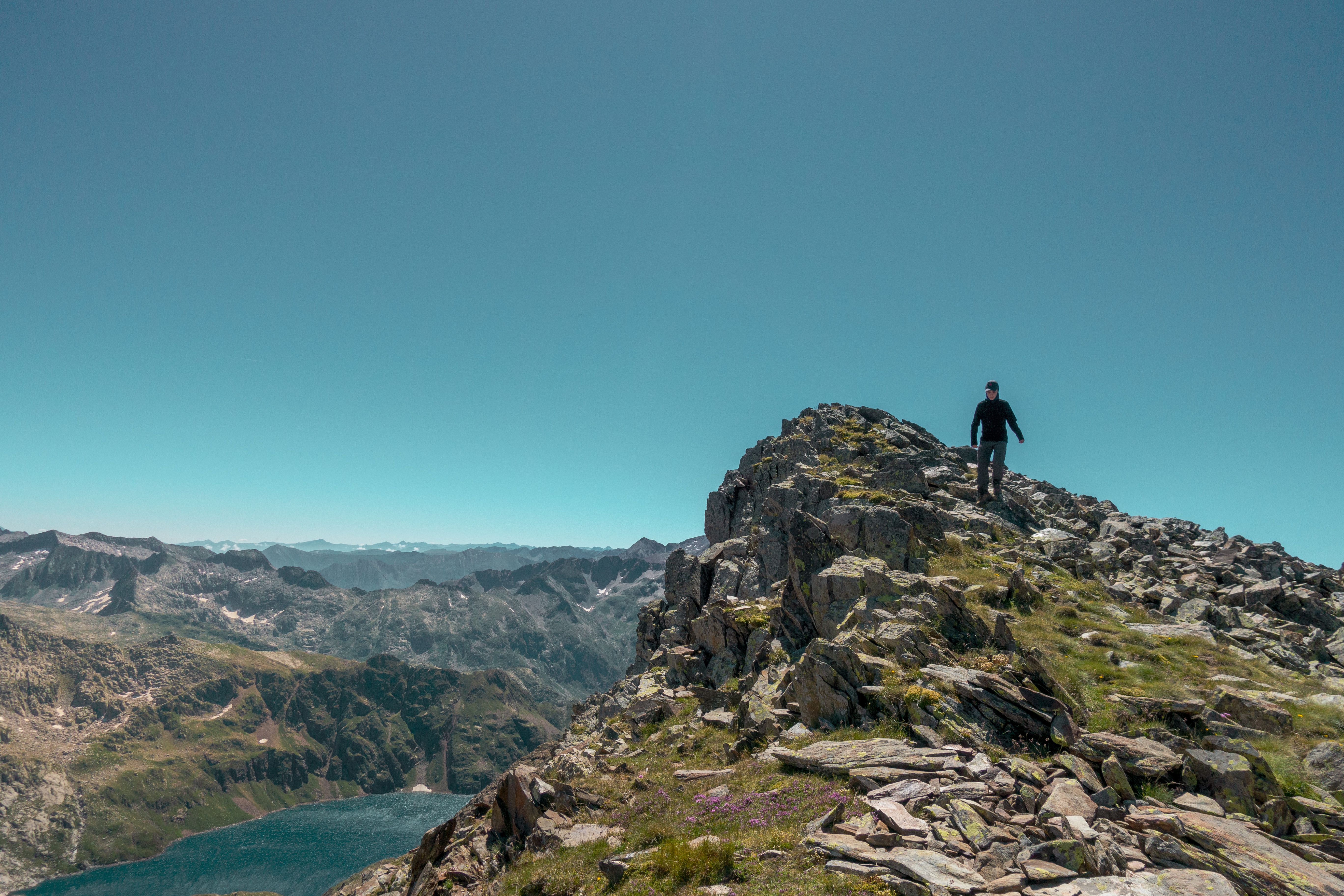 Man Walking down from Mountain Peak above Lake · Free Stock Photo