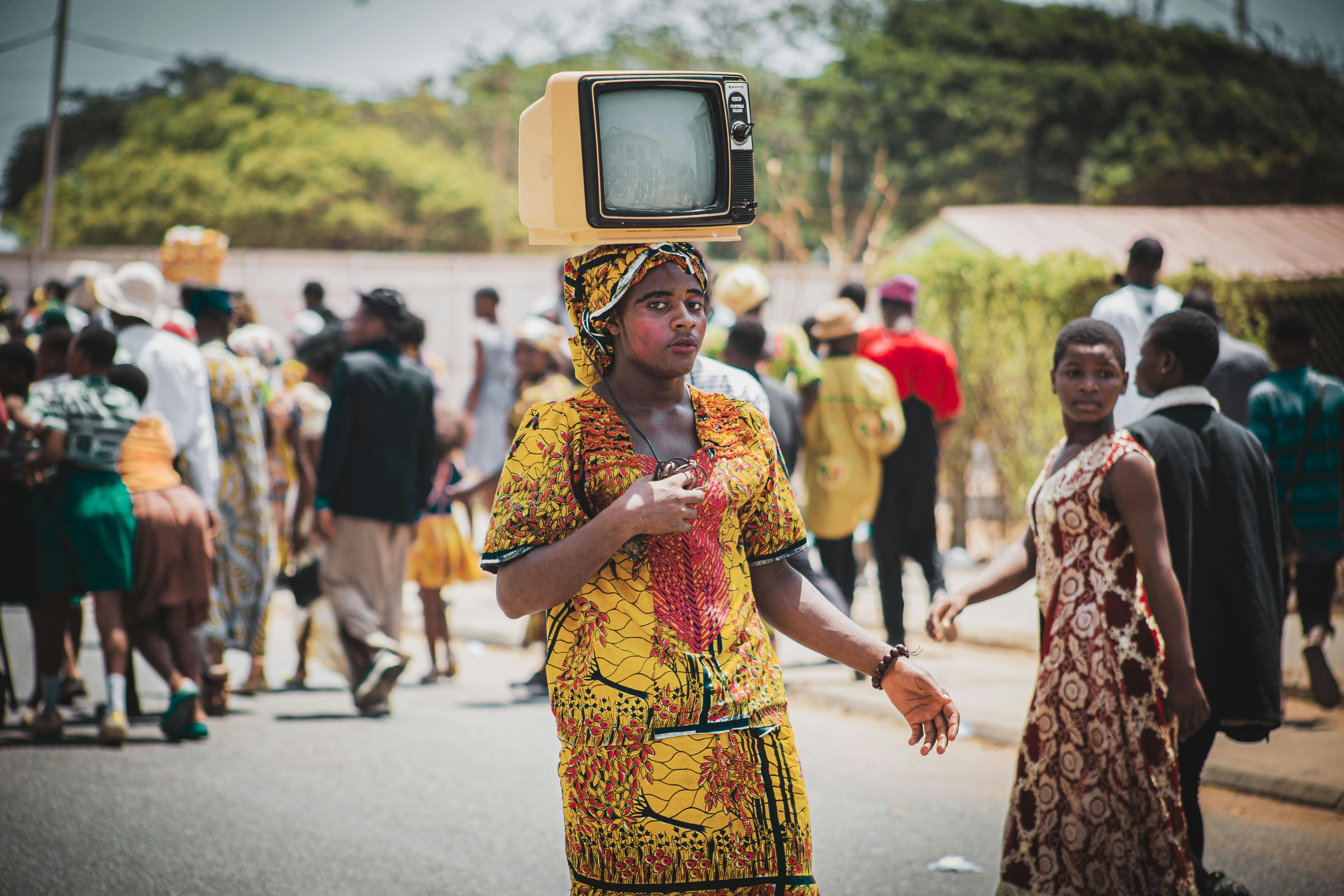 Man in a Dress Walking in the Crowd and Carrying a TV on His Head ...