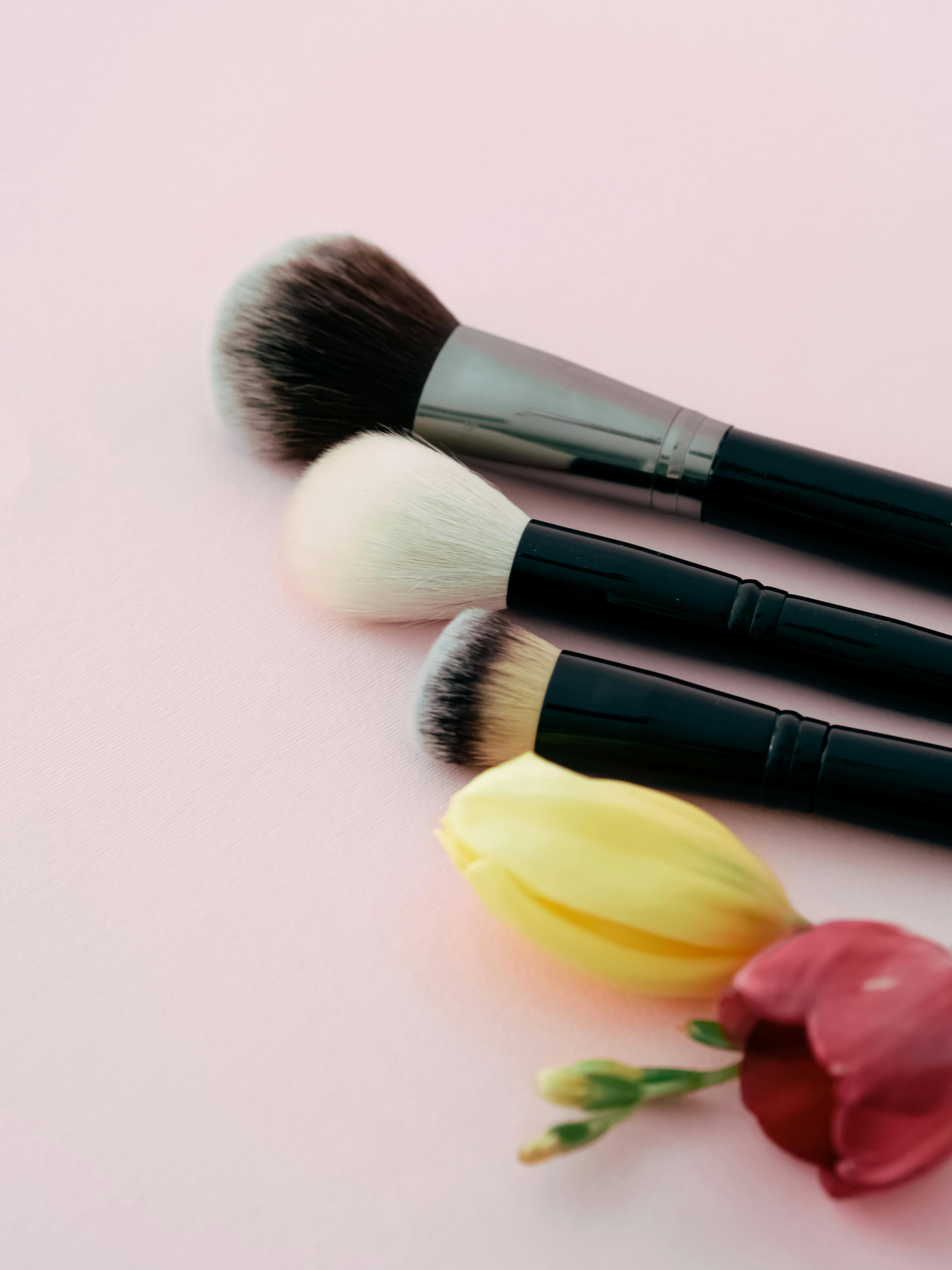 Makeup Brushes in Row by Flowers on Pink Background · Free Stock Photo