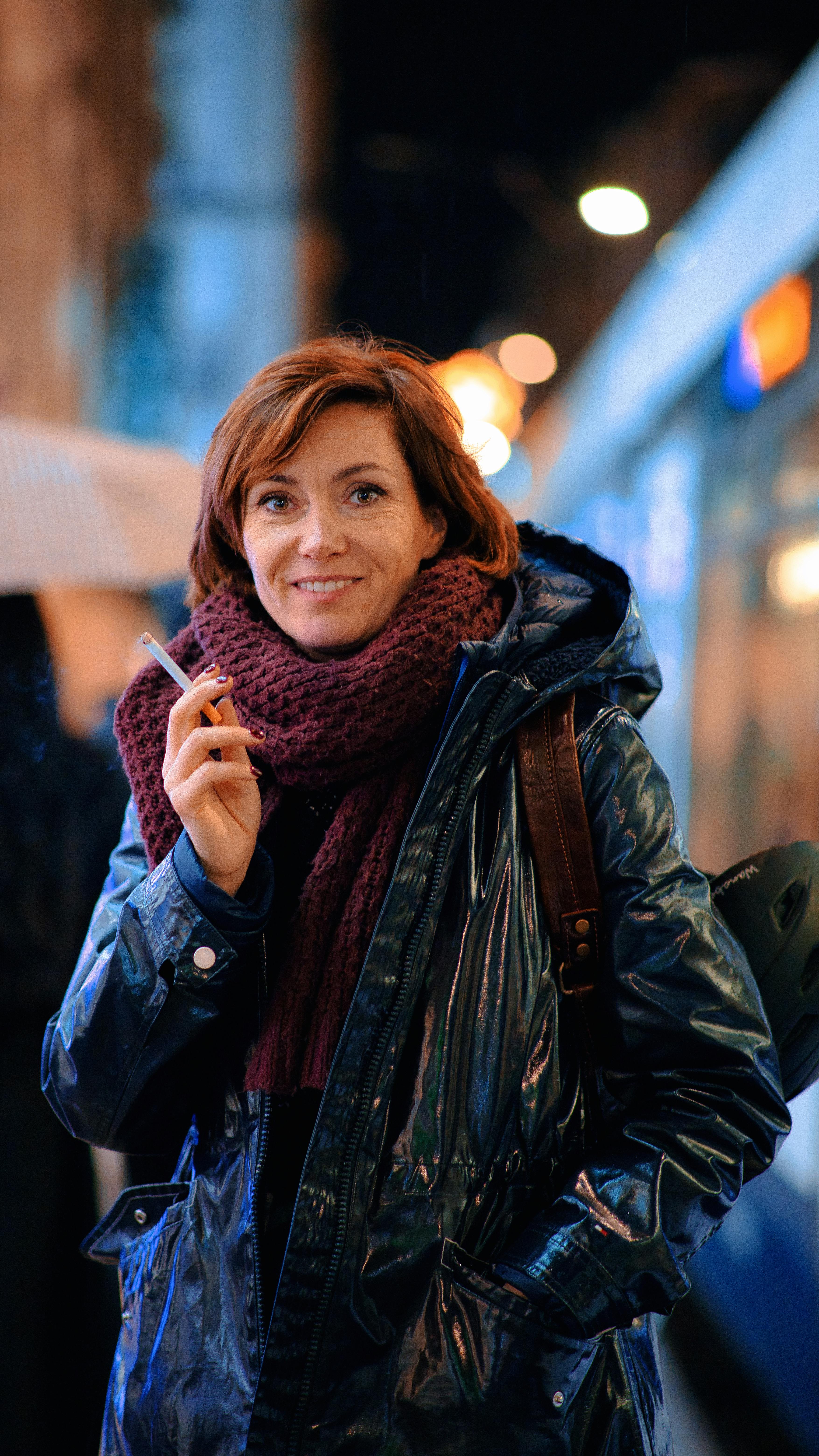 A woman in a coat and scarf smoking a cigarette · Free Stock Photo