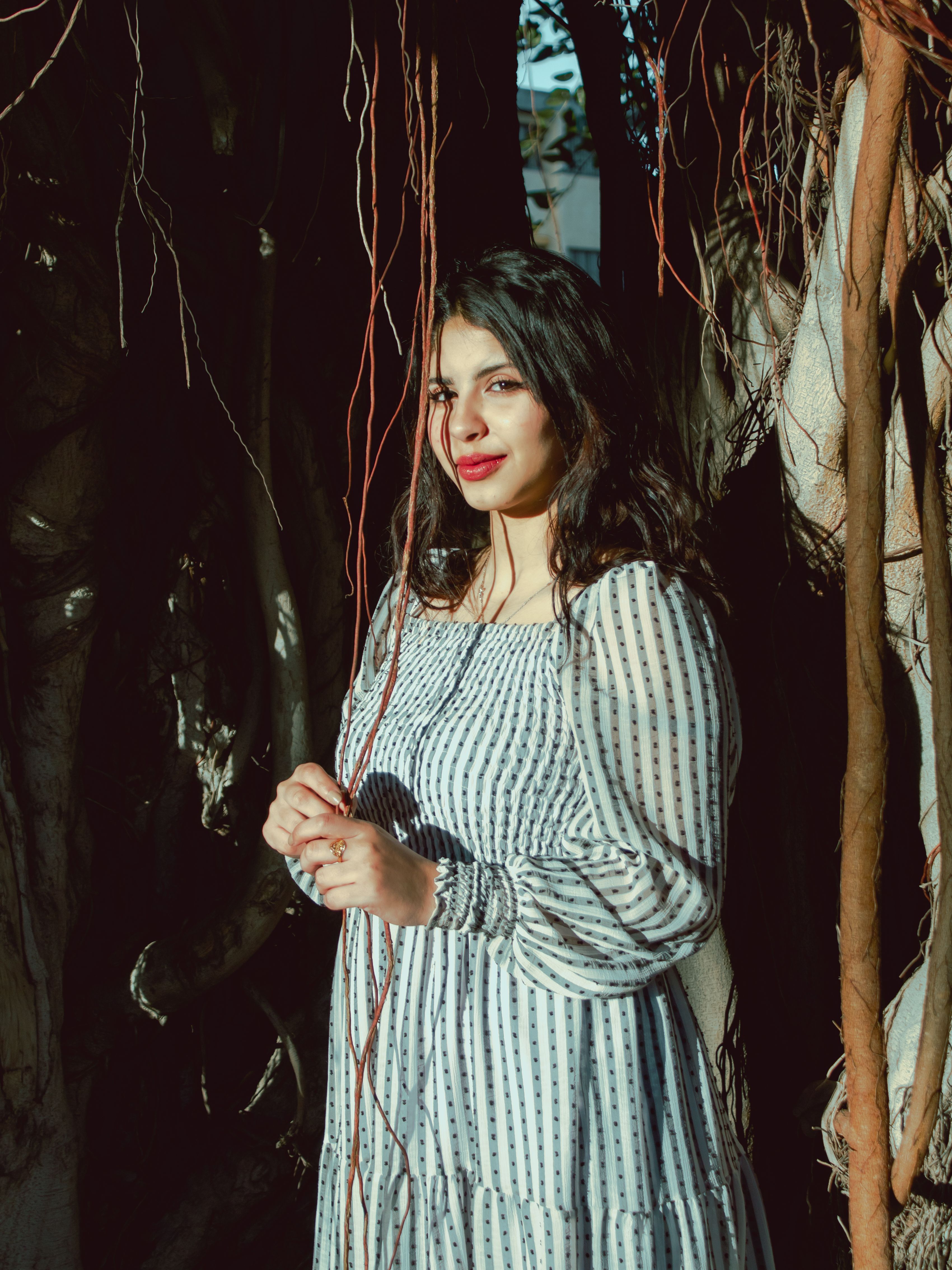 Woman Wearing a Striped Dress, Standing under Tree Roots · Free Stock Photo