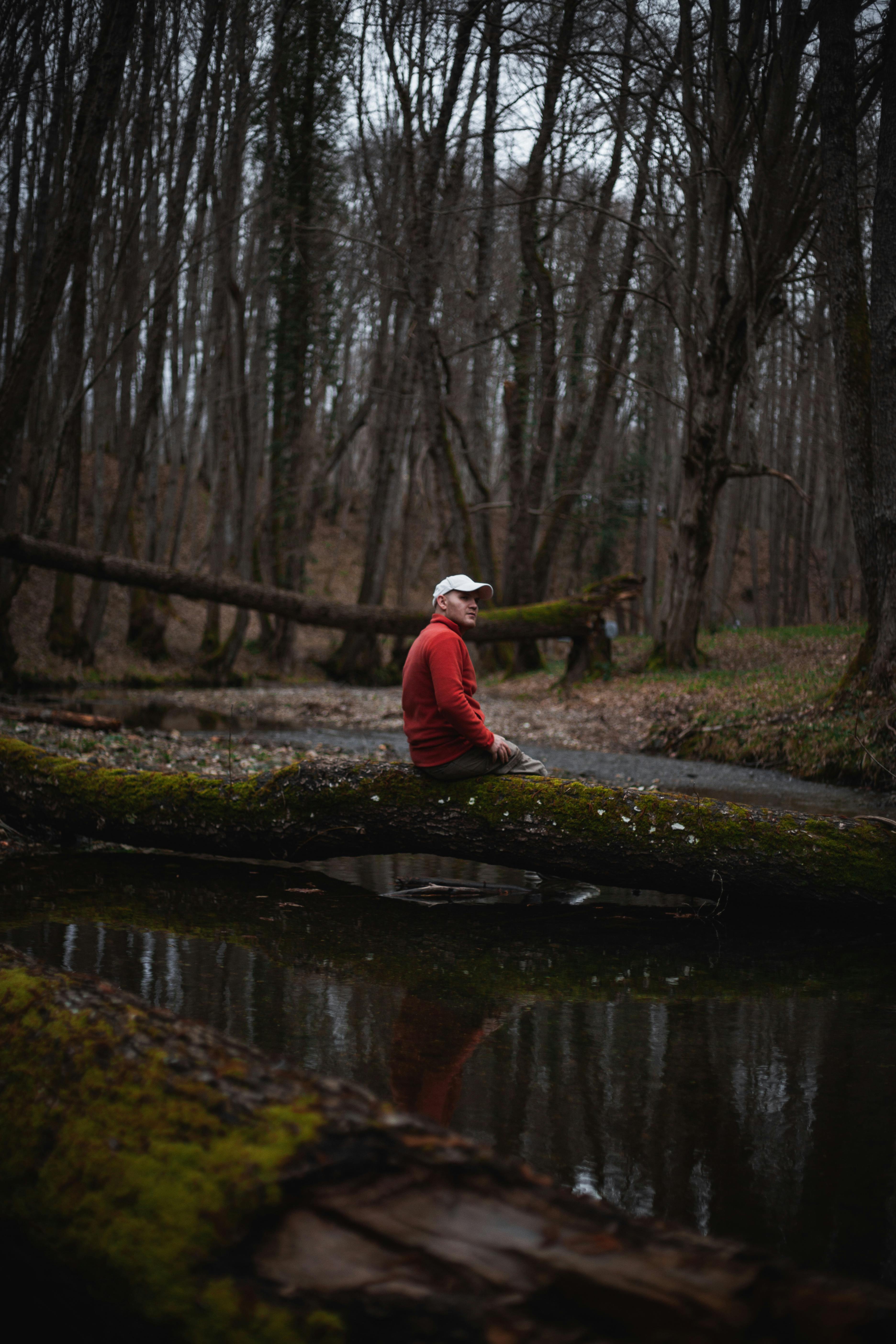 Man in Red Jacket Sitting on Tree Log by River · Free Stock Photo