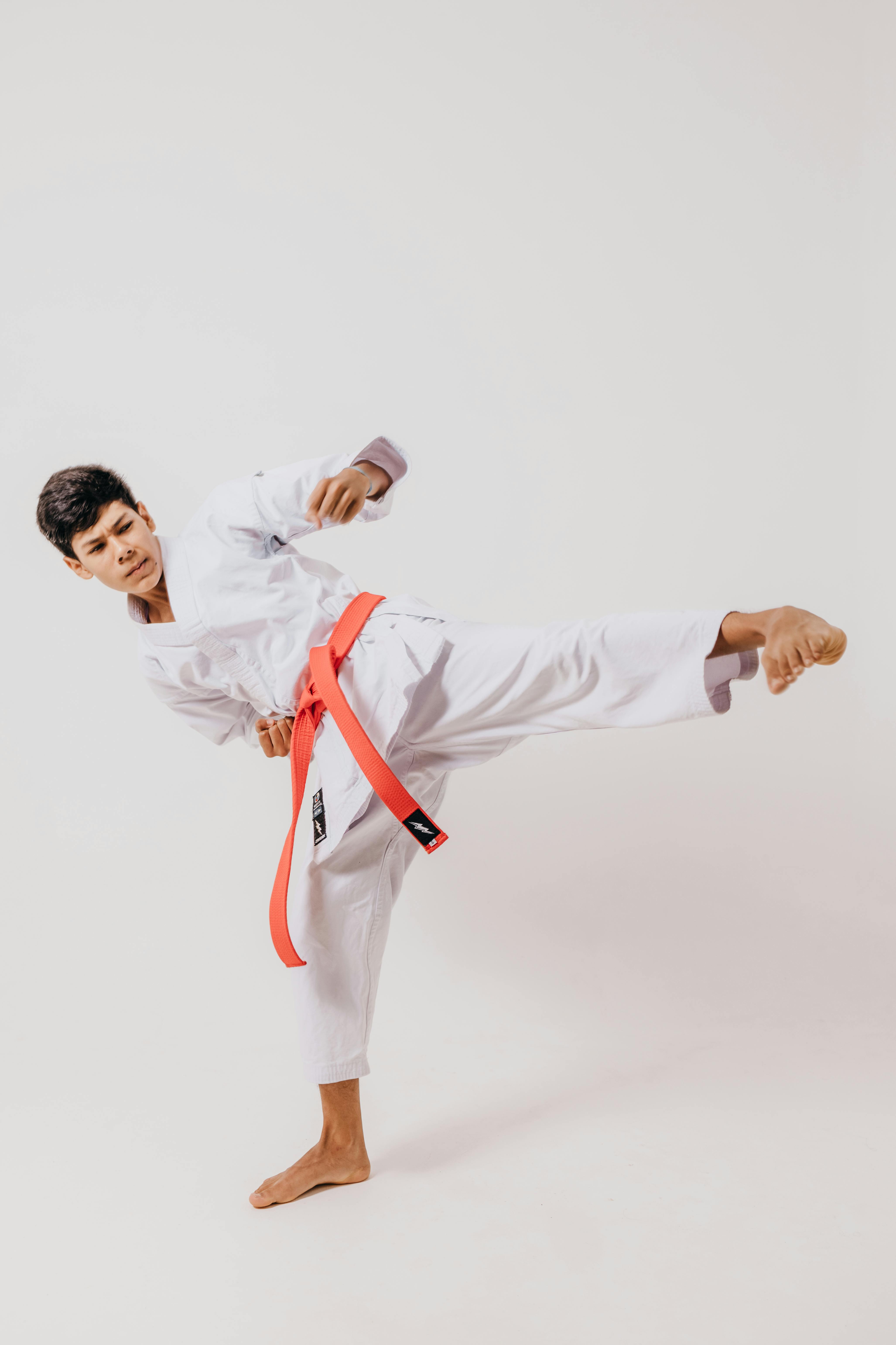 A young boy in a red belt is doing a kick · Free Stock Photo