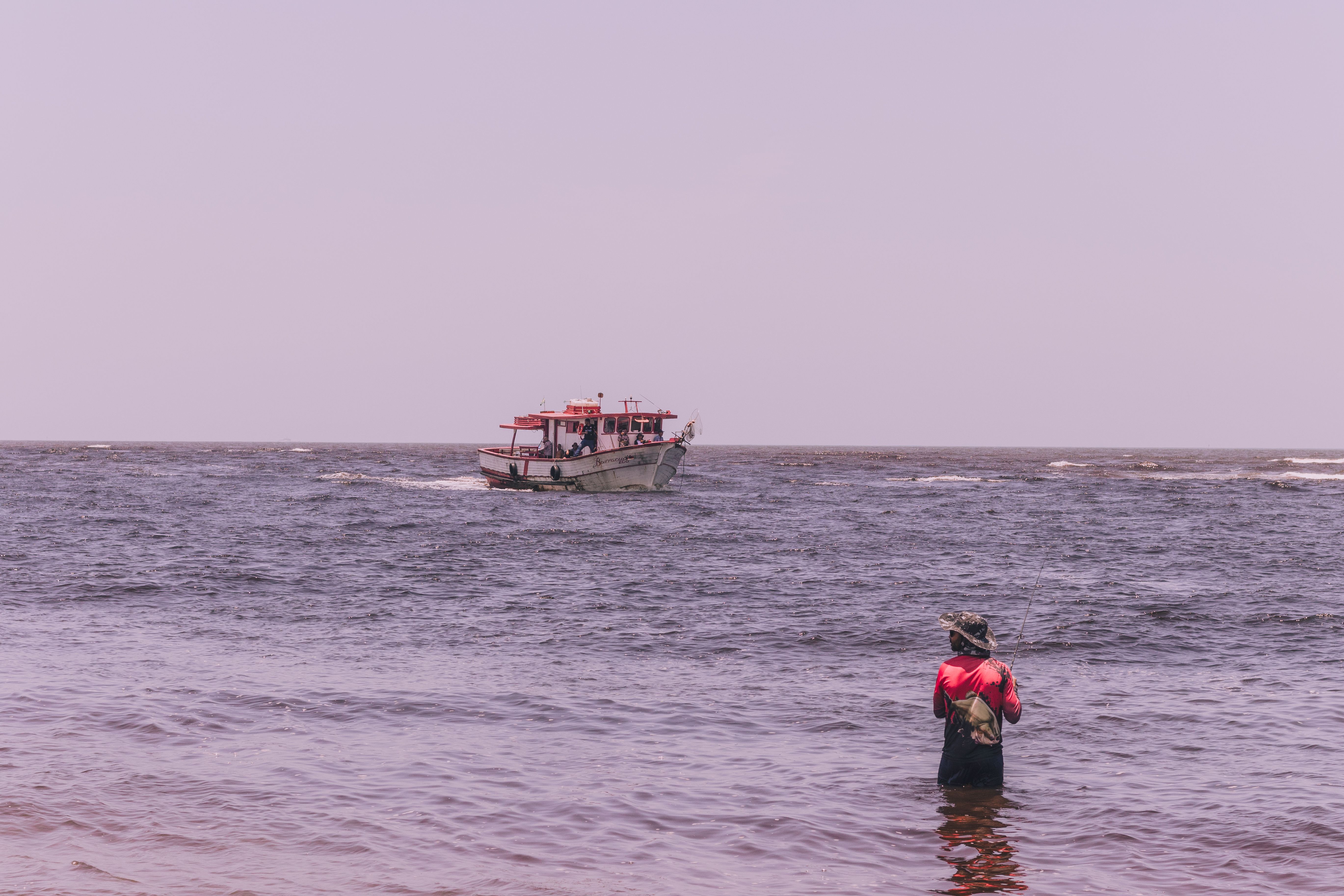 Man Standing in a Sea and Fishing and a Fishing Boat Riding in Distance ...