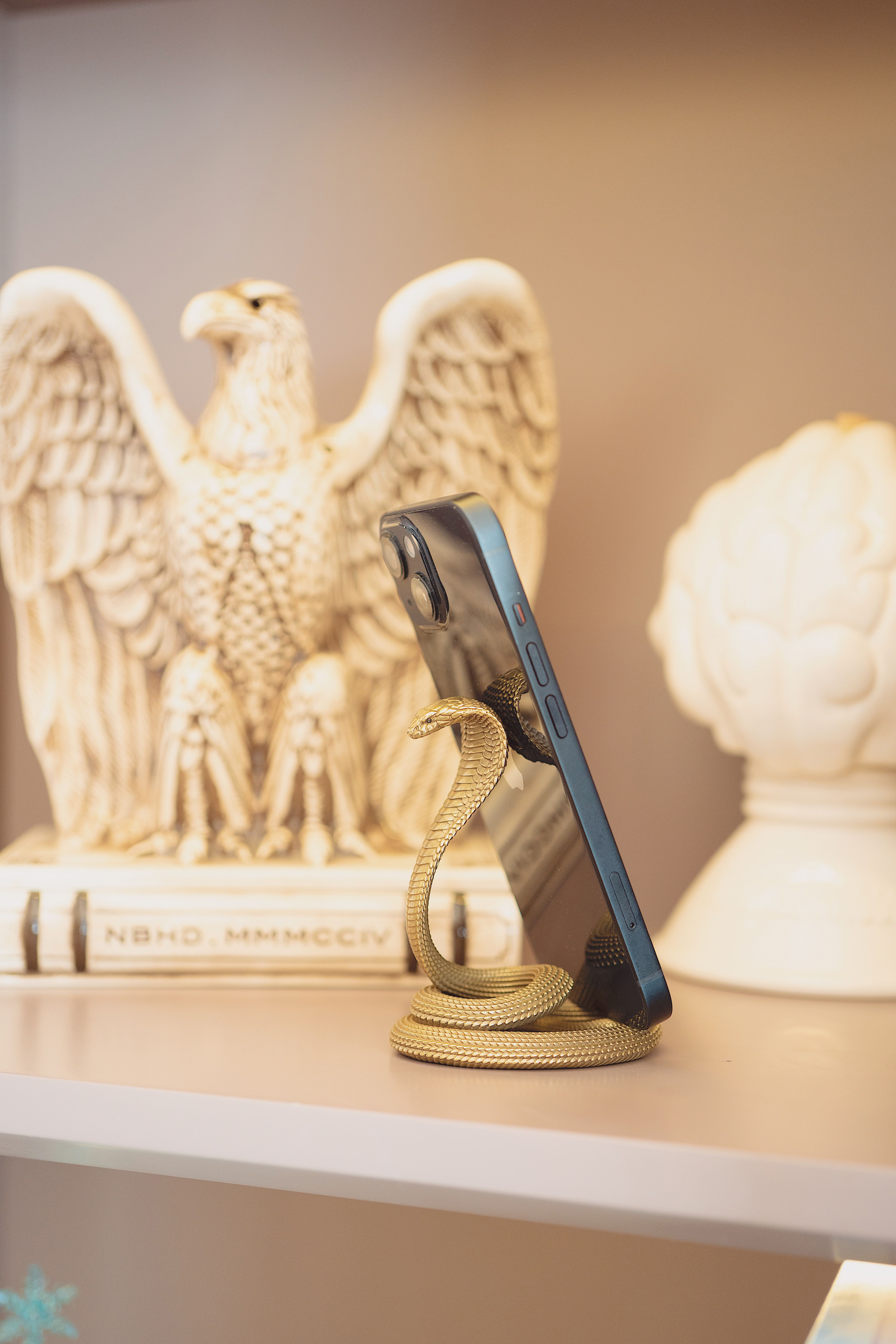 Snake-shaped Phone Stand with a Smartphone on a Shelf with Statuettes ...