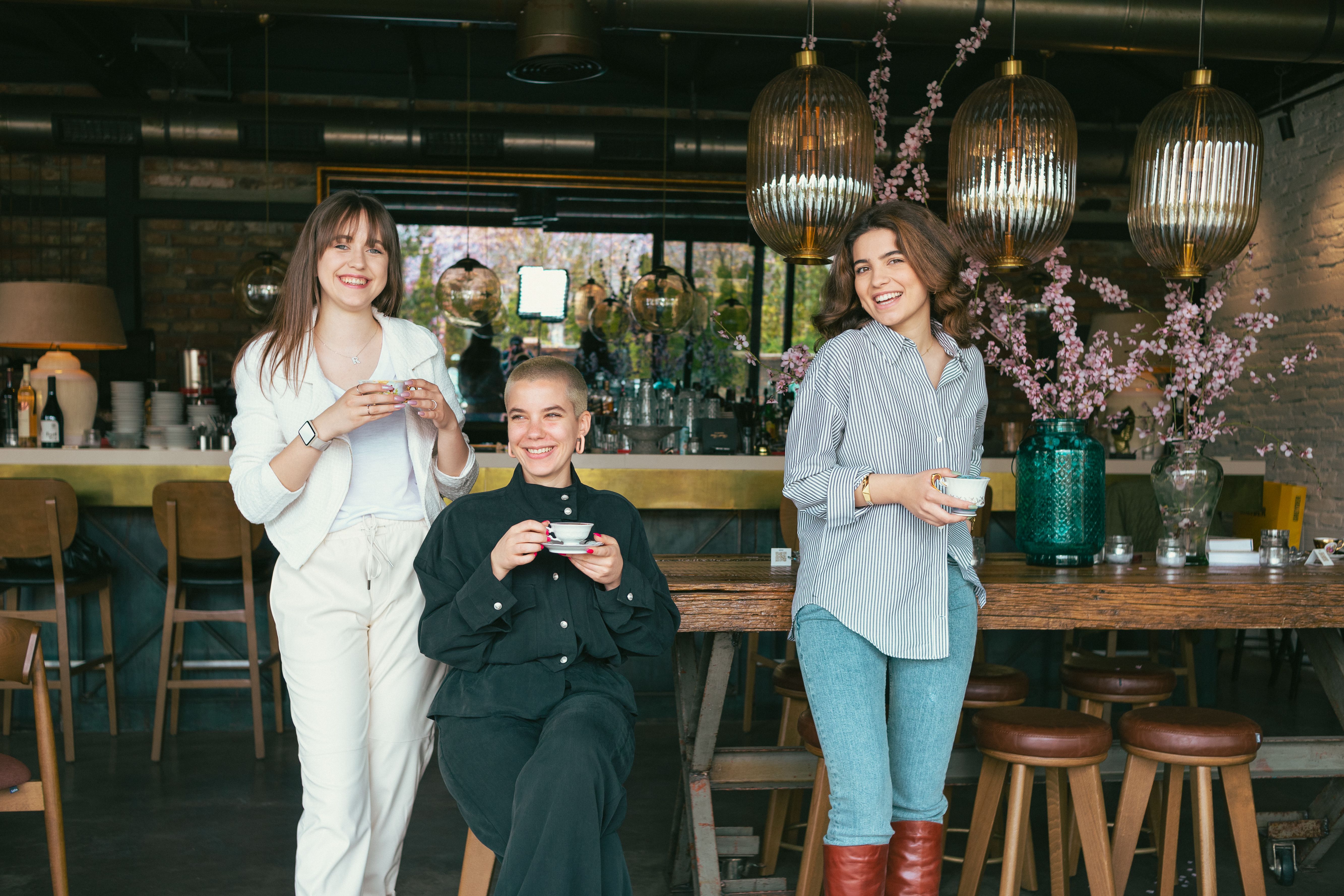 Smiling Models Posing with Cups at Cafe · Free Stock Photo