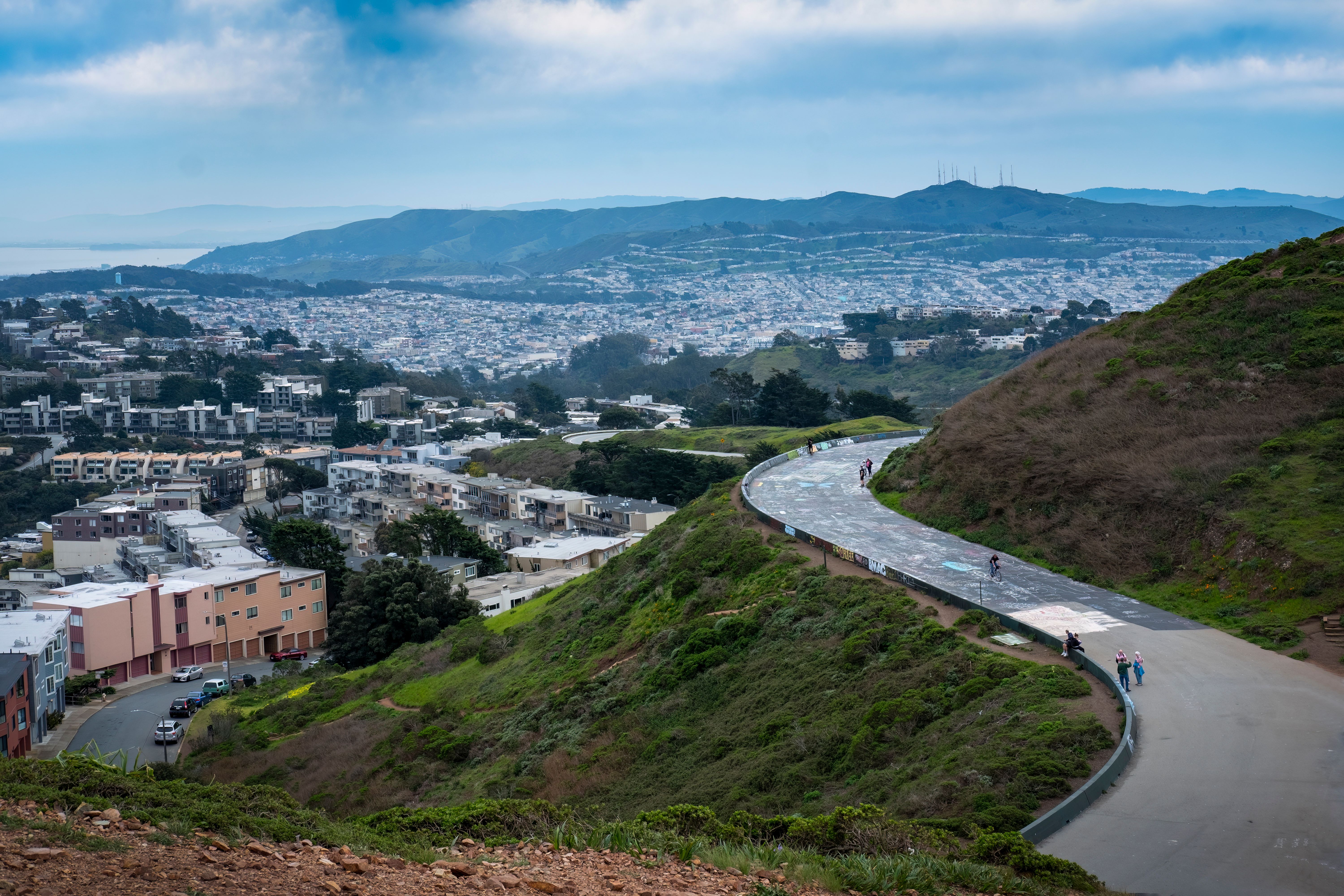 Road Curve on Hillside Against City · Free Stock Photo
