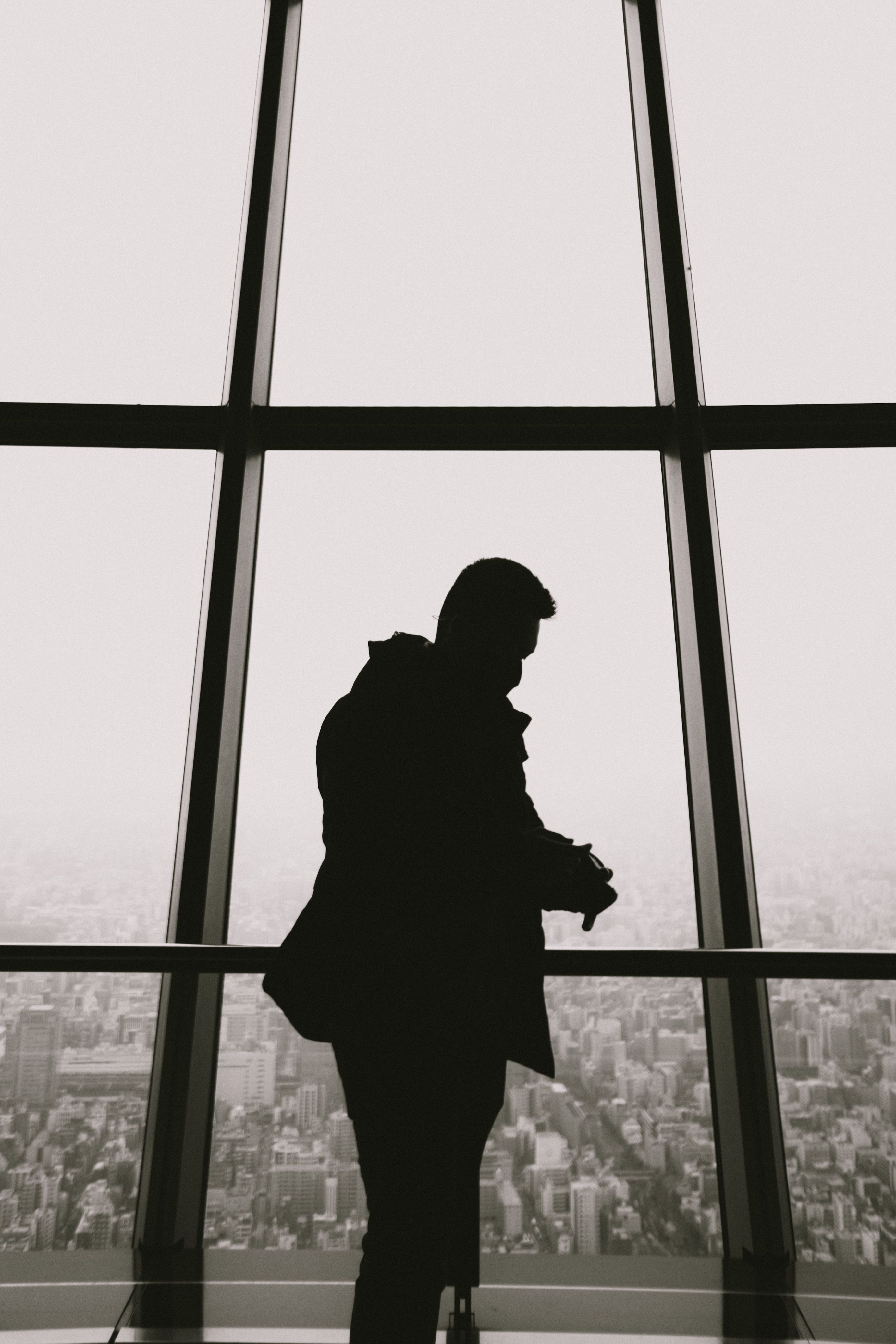 Silhouette of a Man Standing next to a Window on a High Floor of a ...