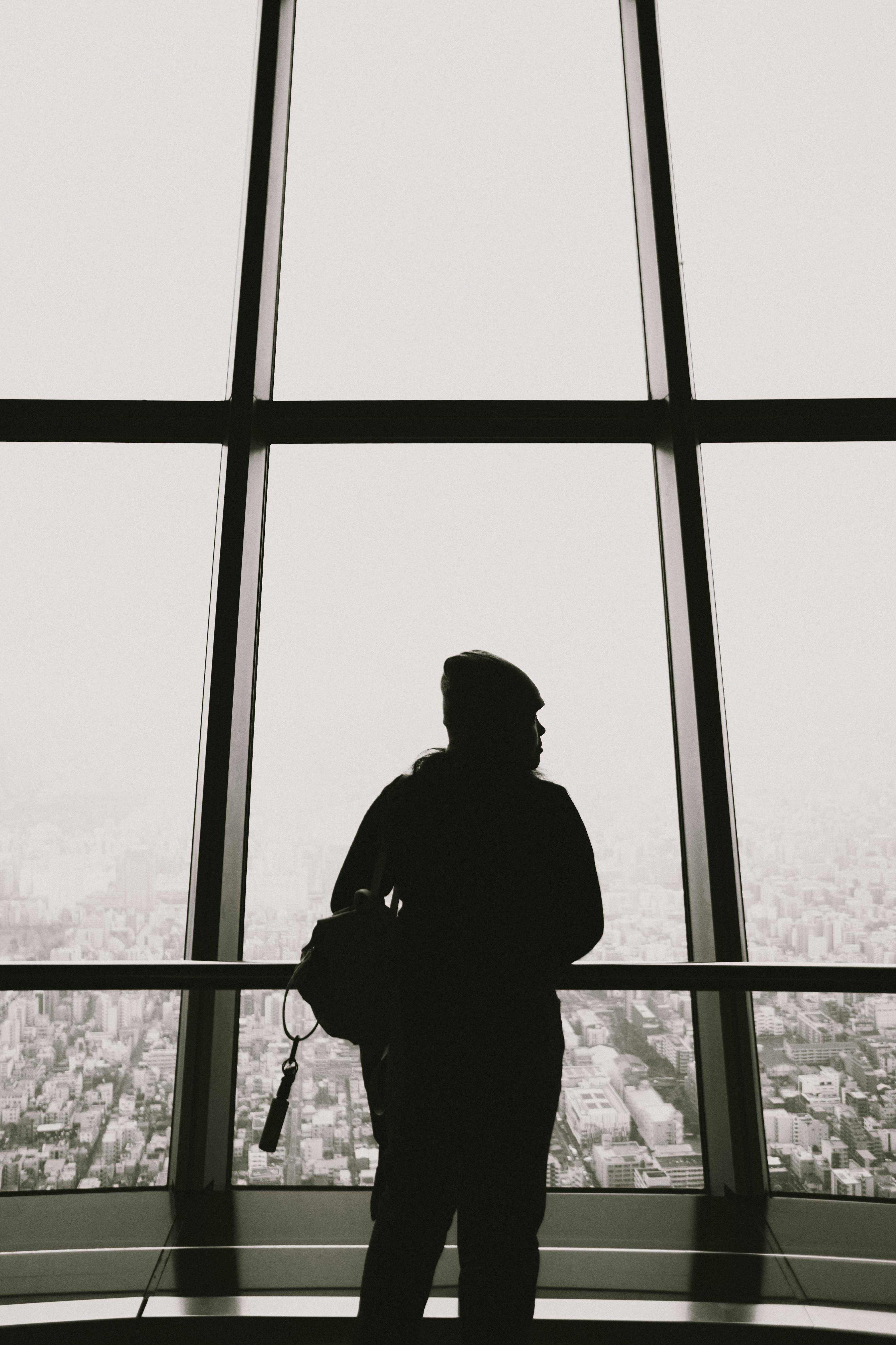 Man Standing and Looking at a Cityscape from a Window · Free Stock Photo