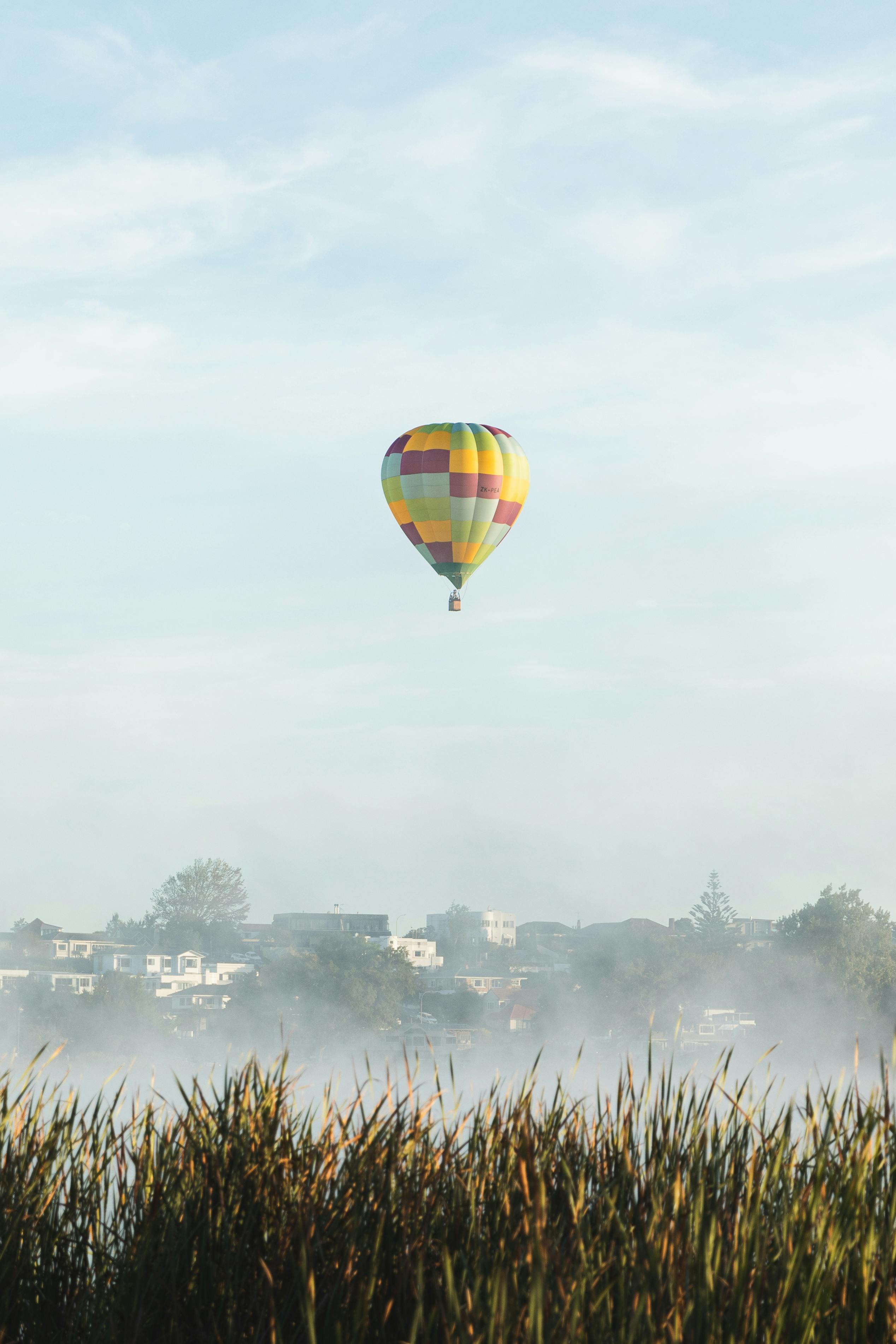 Checkered Hot Air Balloon Flying Above the Foggy City · Free Stock Photo