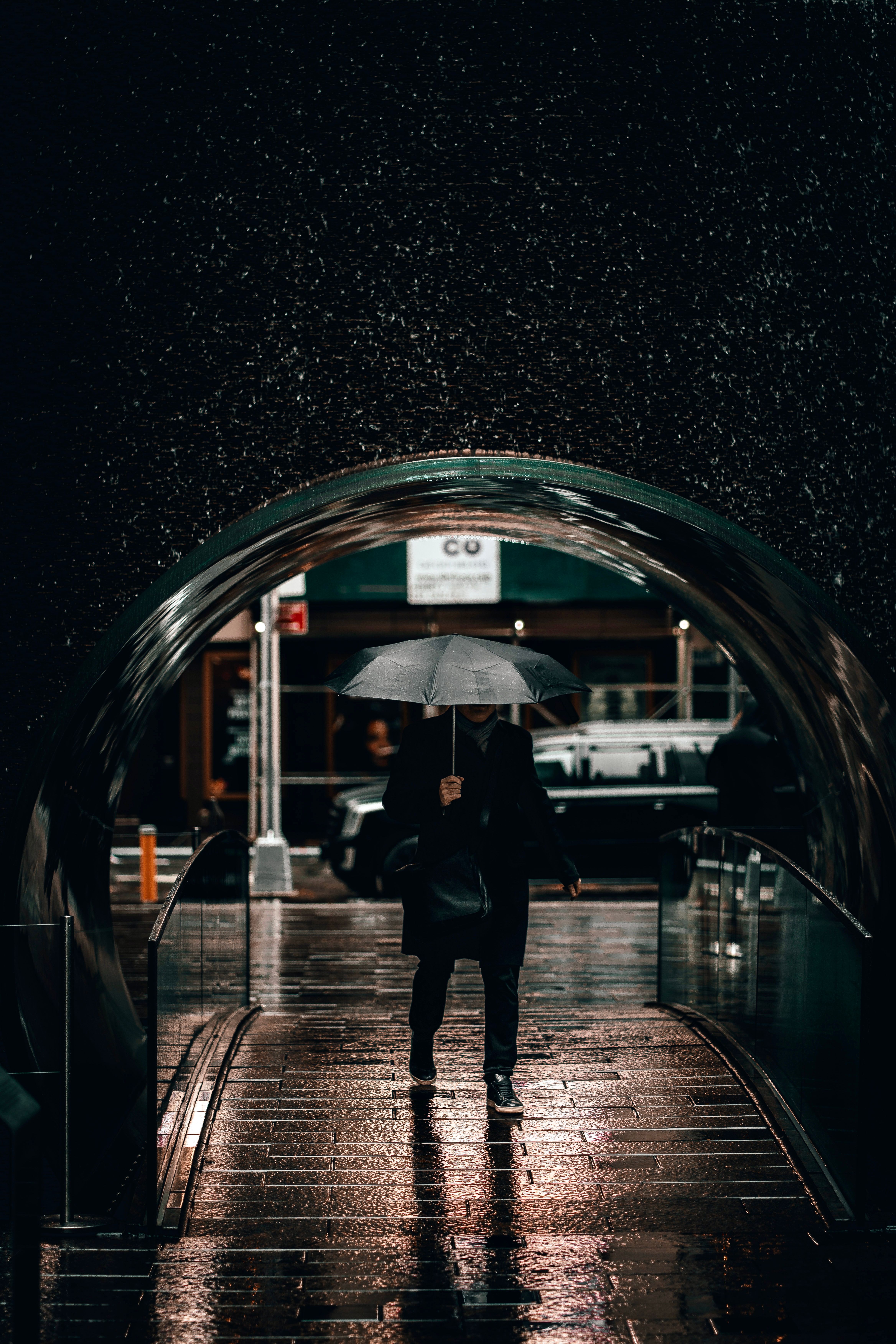 Man Walking on a Roofed Footbridge in Rain at Night · Free Stock Photo