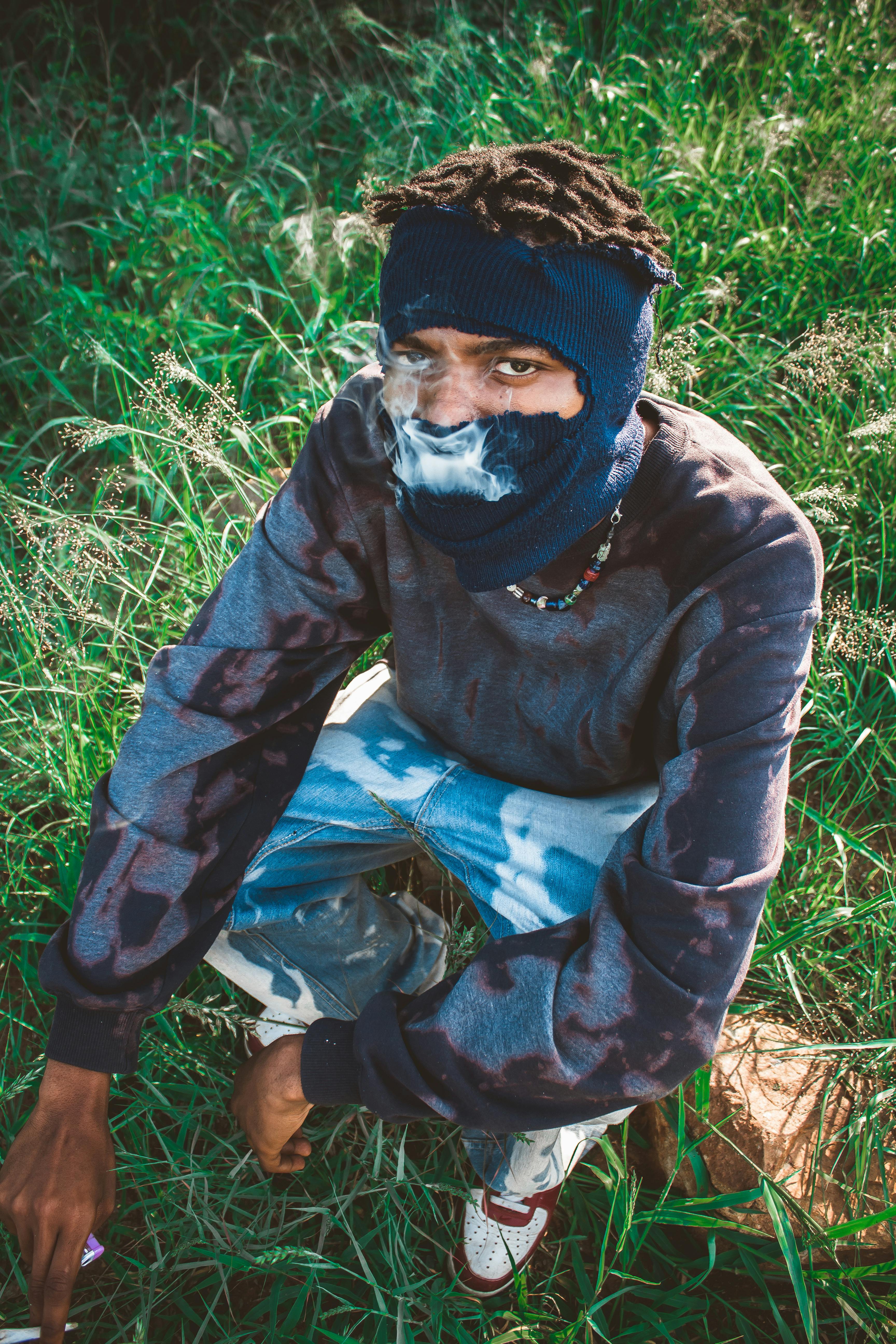 Man with Dreadlocks Smoking a Cigarette Through a Balaclava Sitting in ...