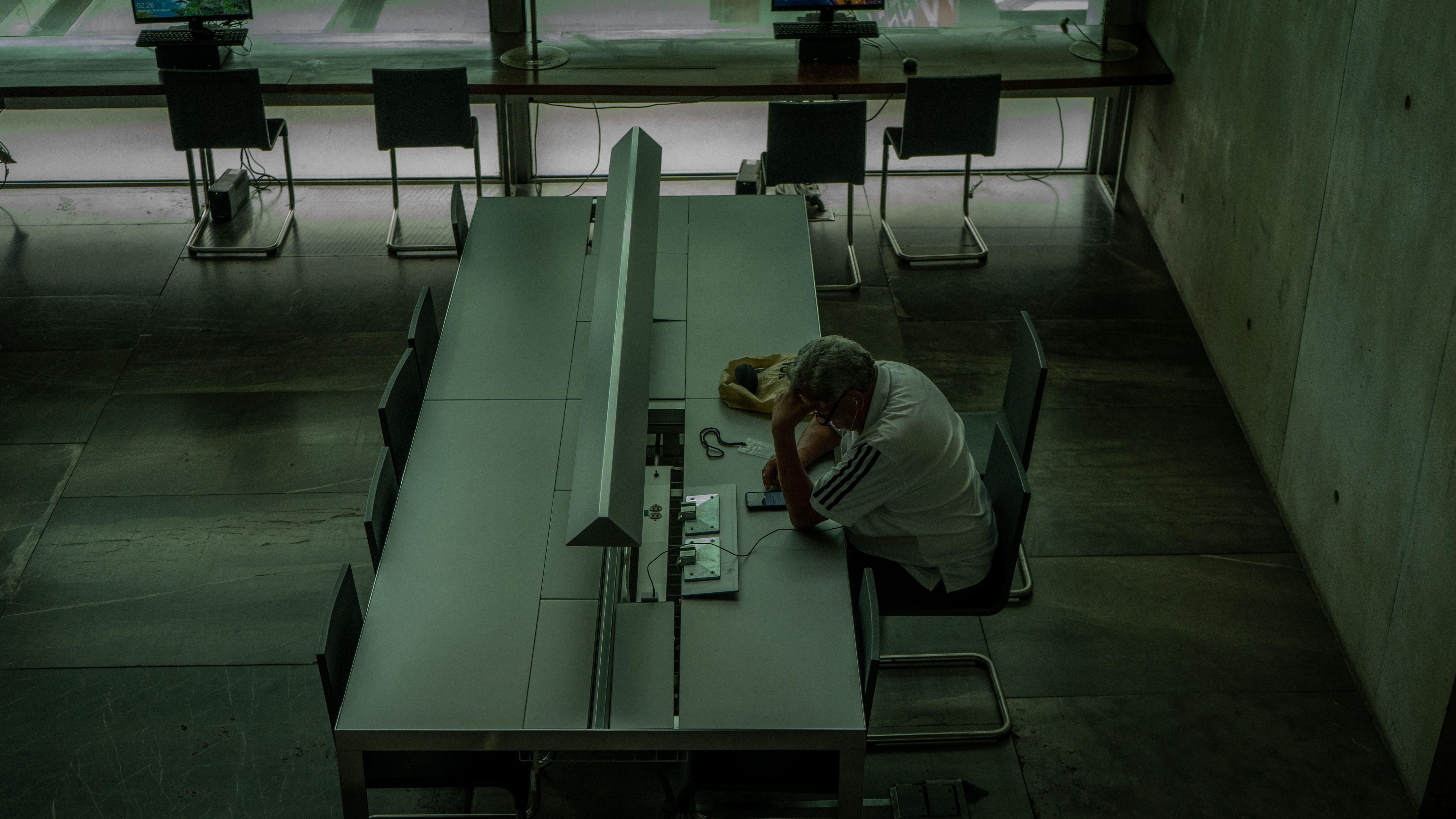 Man Sitting by a Desk and Bending over his Phone · Free Stock Photo