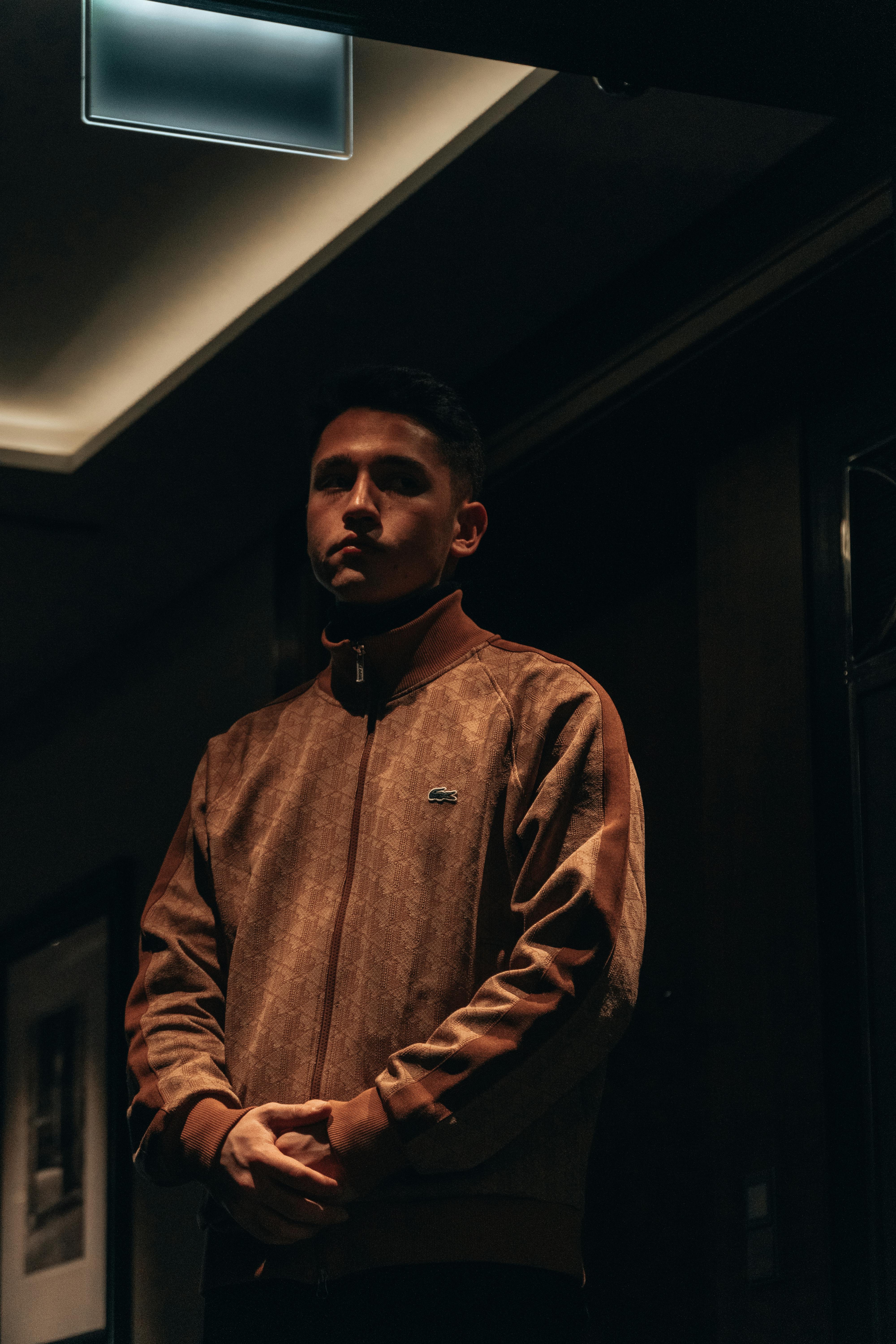 Young Man Standing under a Light in a Dark Corridor · Free Stock Photo