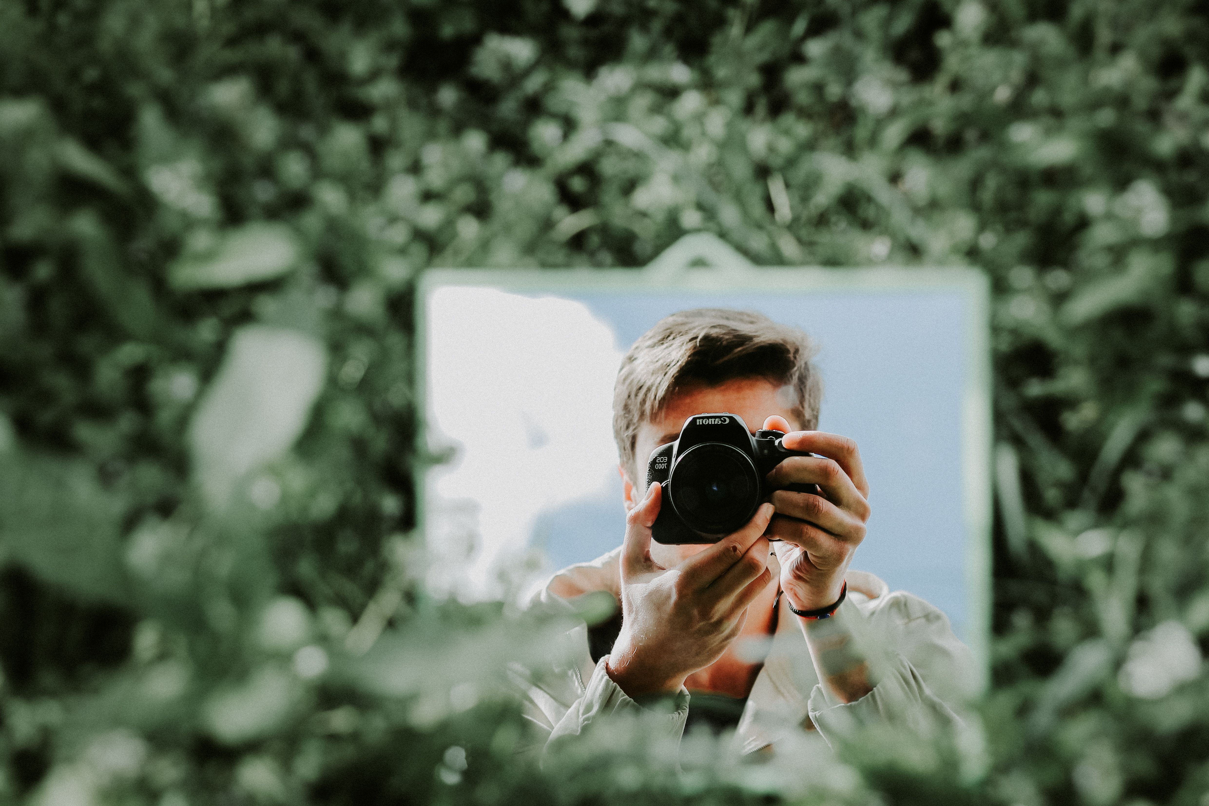 Man Using a Camera Reflecting in a Mirror Standing Between Green Trees ...