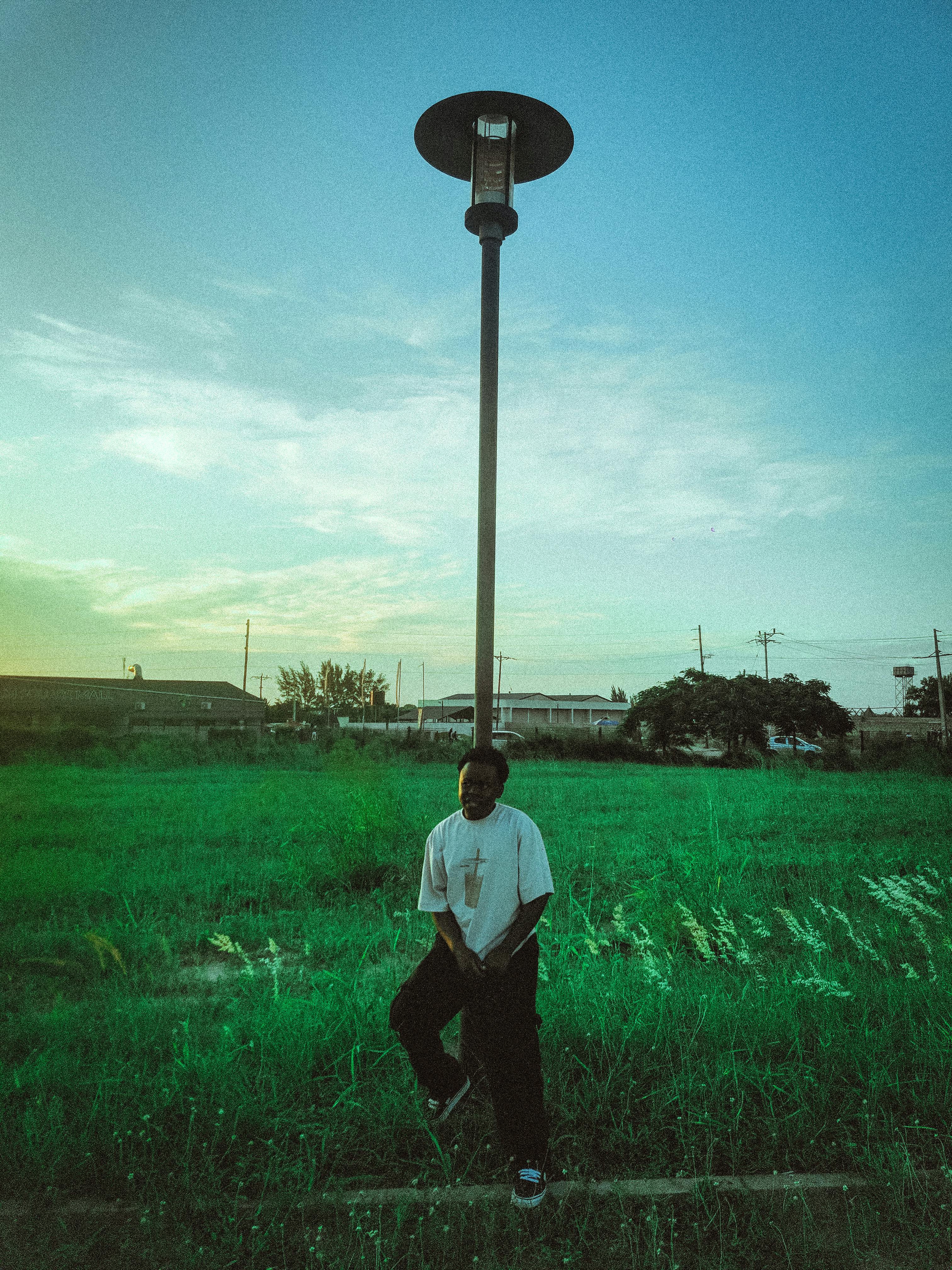 Boy Leaning against a Lamp Post in a Meadow · Free Stock Photo