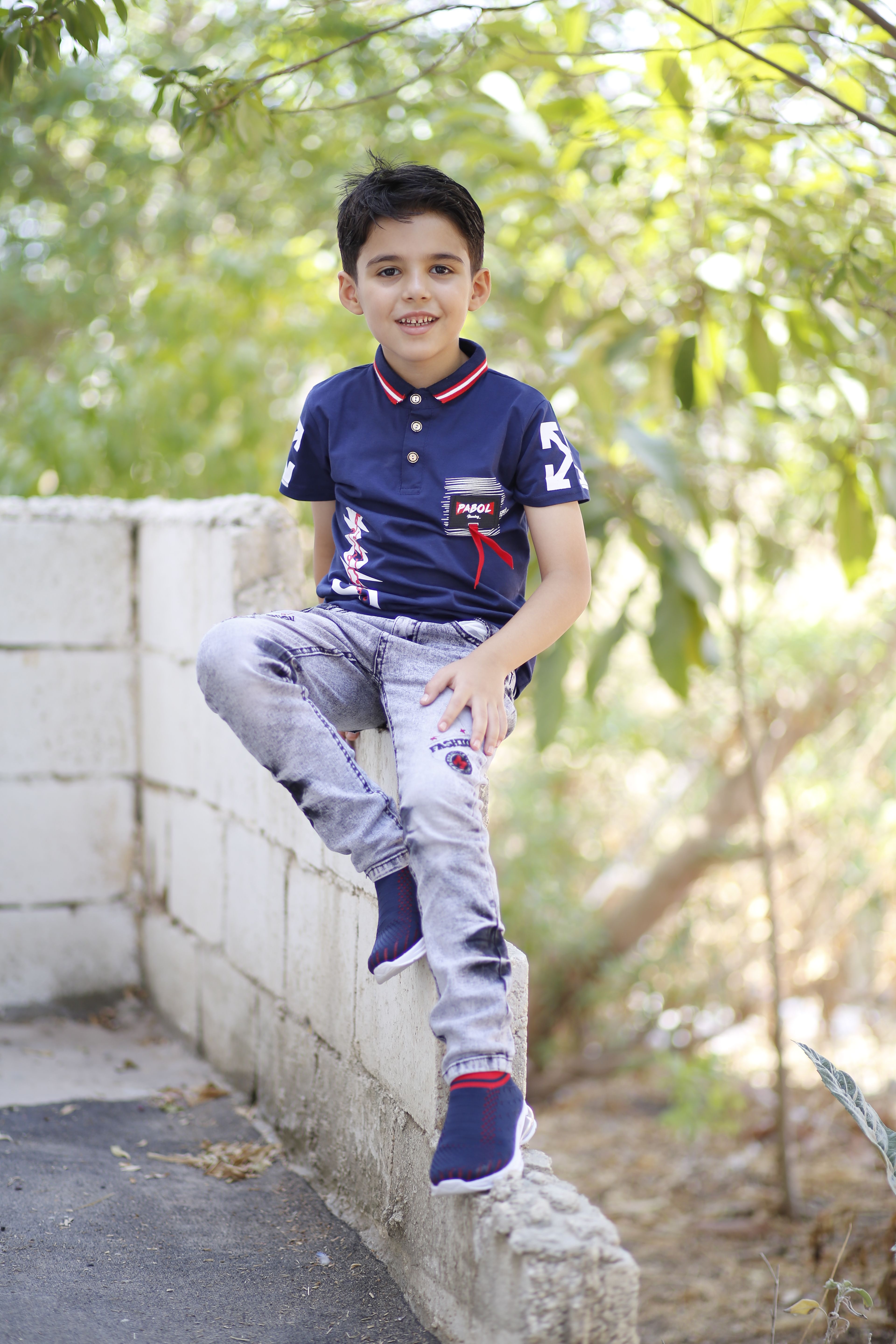Boy Sitting on Wall with Trees behind · Free Stock Photo