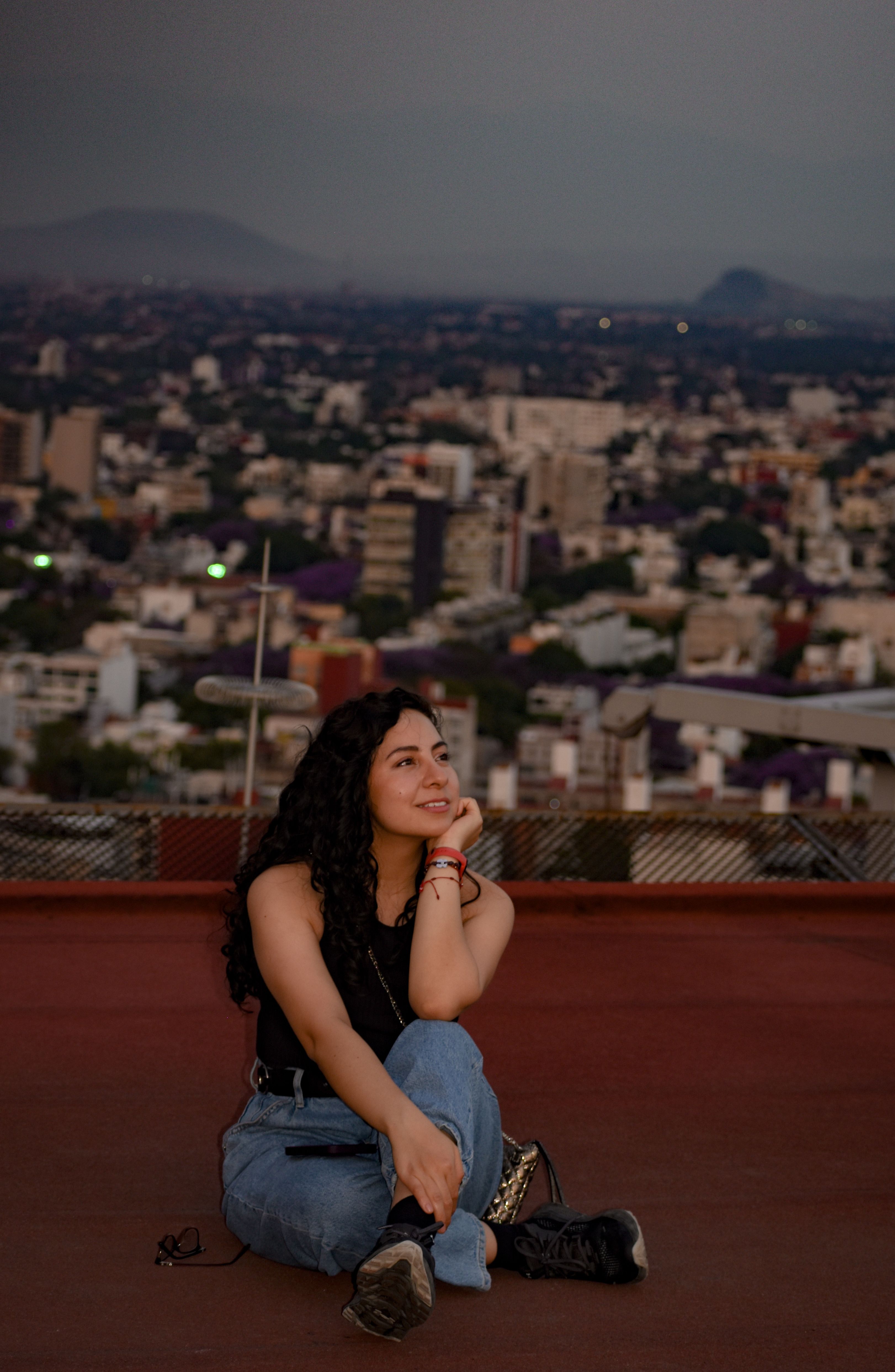 Brunette Woman Sitting on Roof with Town behind · Free Stock Photo
