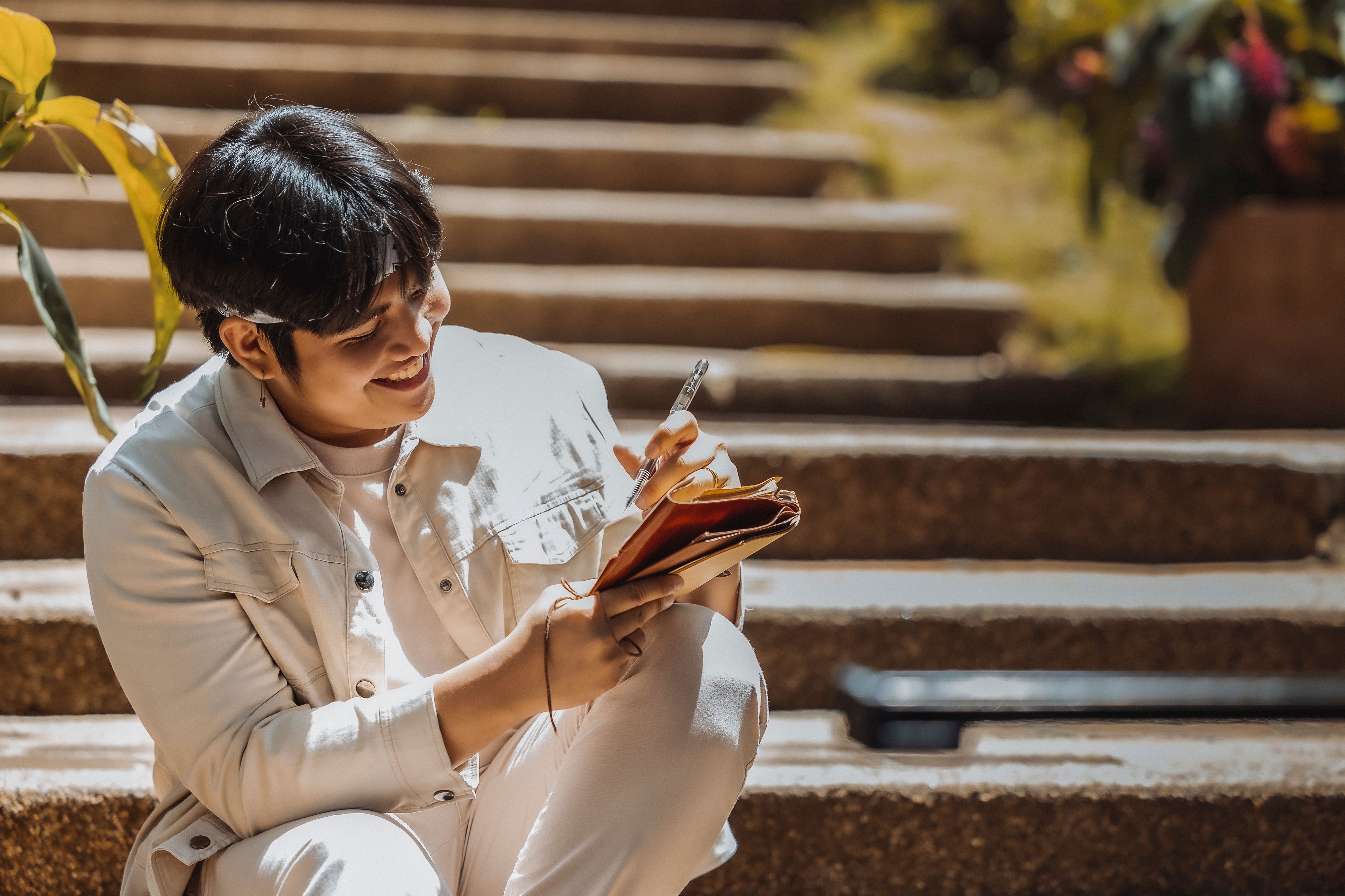 Smiling Man Sitting on Stairs and Writing · Free Stock Photo