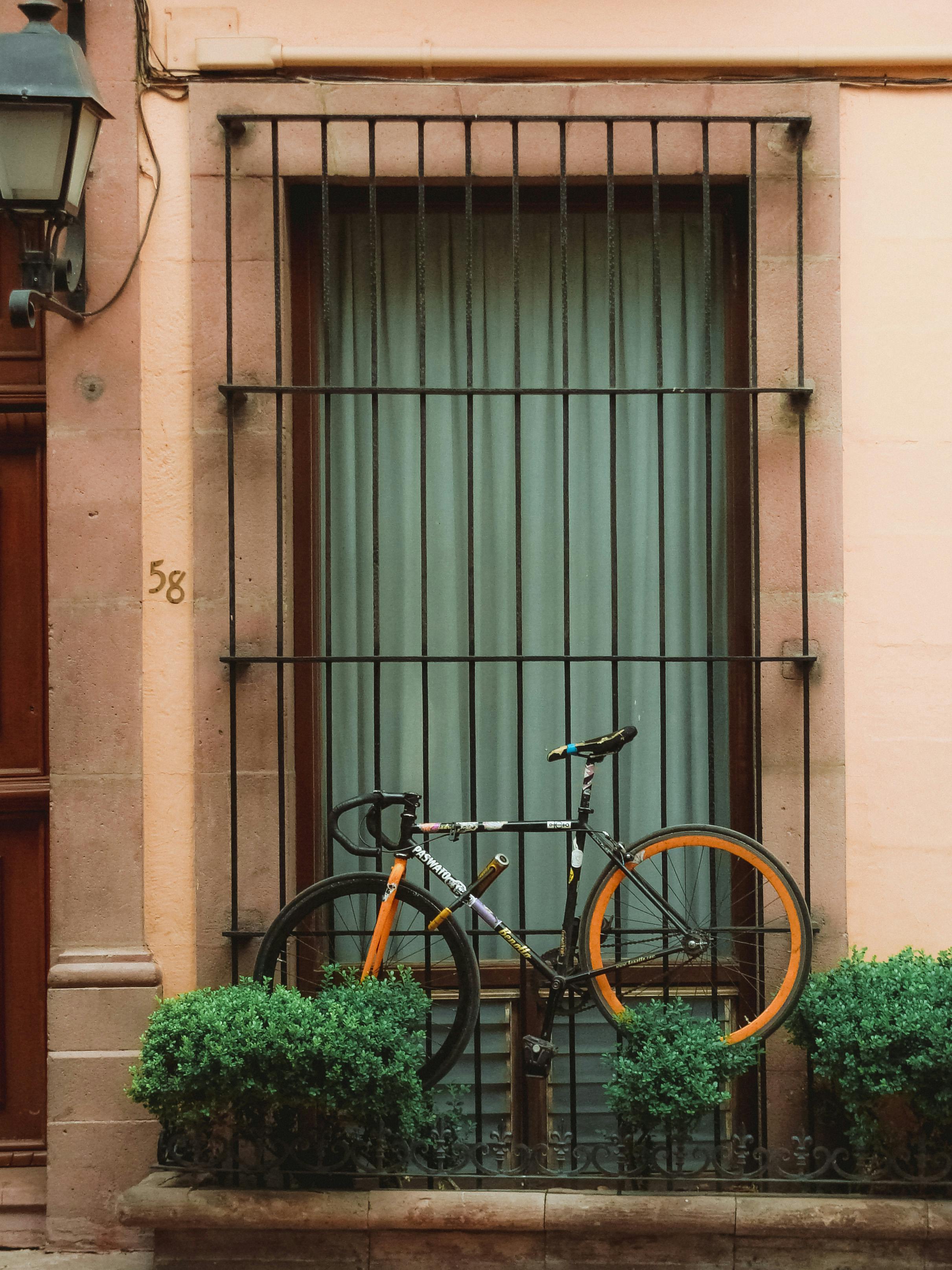 Folding Bicycle Under a Barred Window · Free Stock Photo