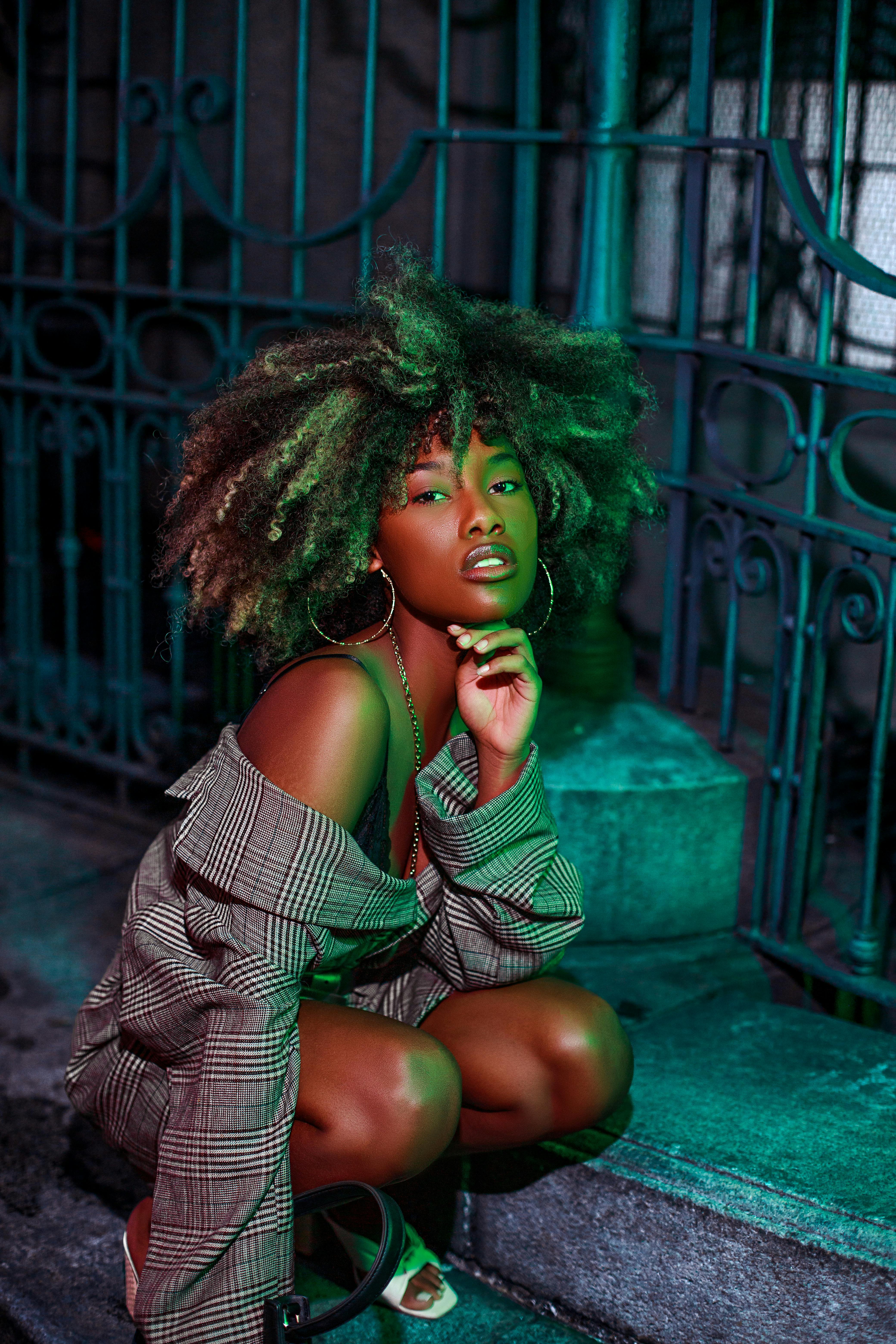 Photo of a Woman with Afro Hairstyle Crouching by a Metal Gate · Free ...