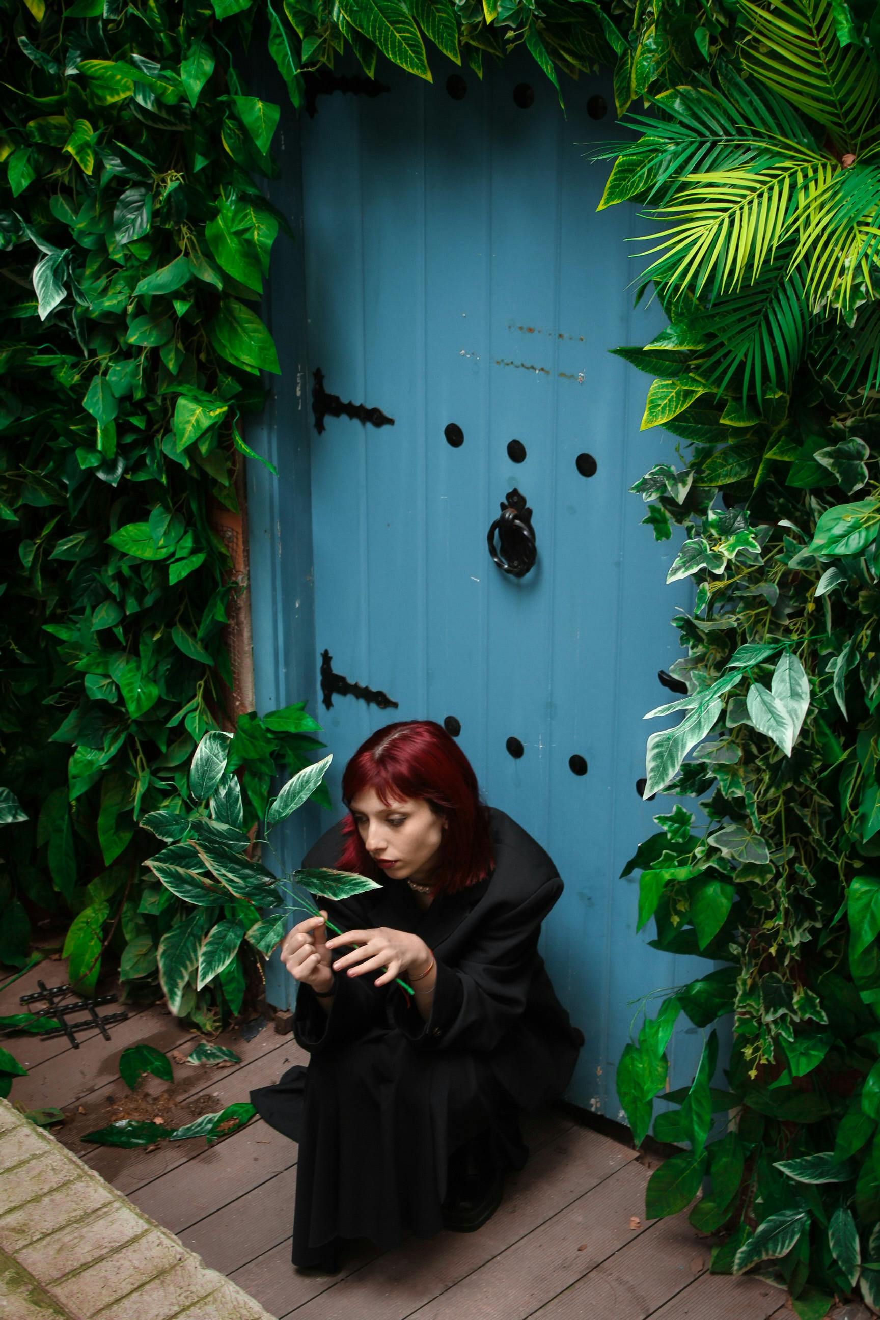 Young Woman Crouching in Front of an Overgrown Door · Free Stock Photo