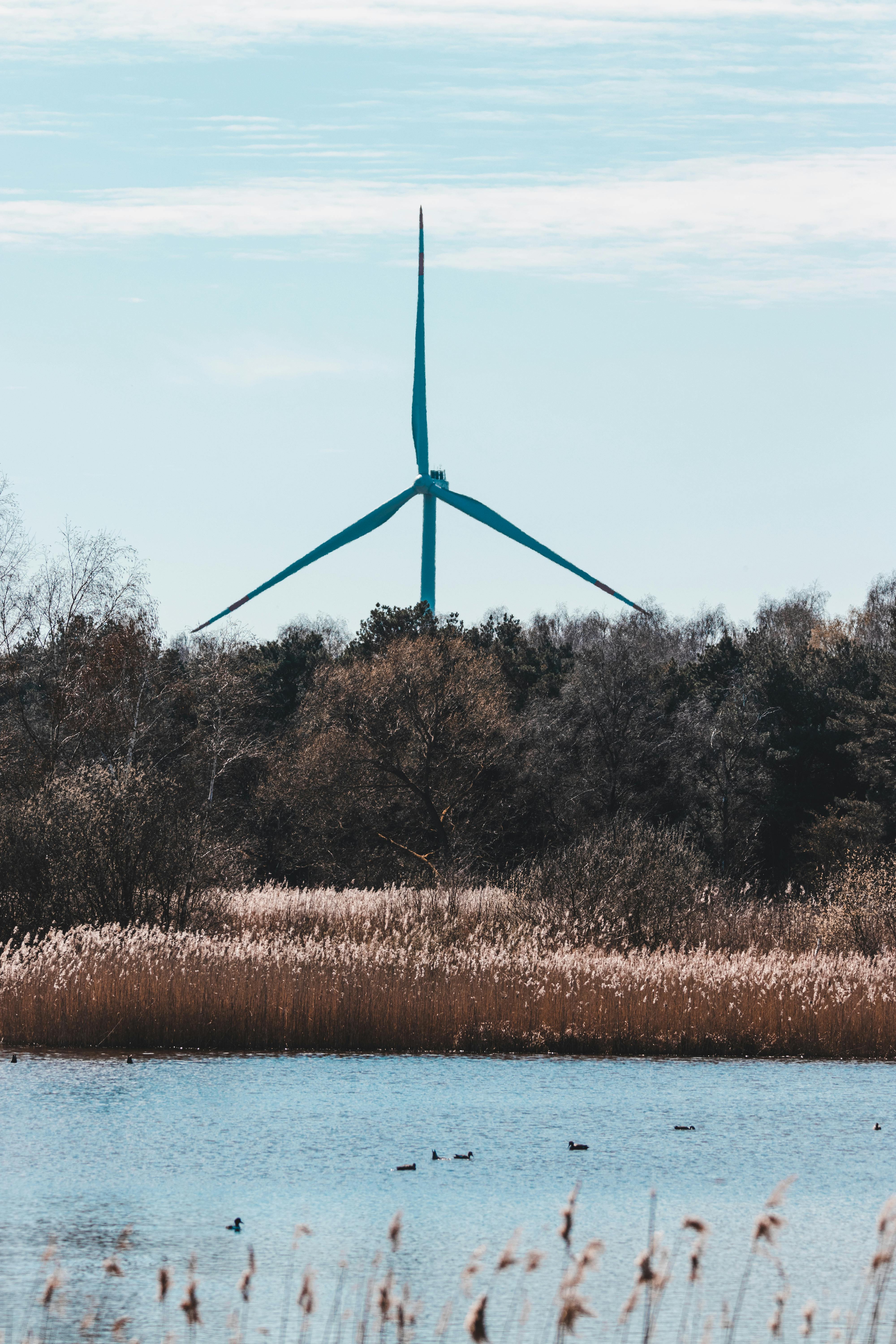 Wind Turbine behind River and Trees · Free Stock Photo