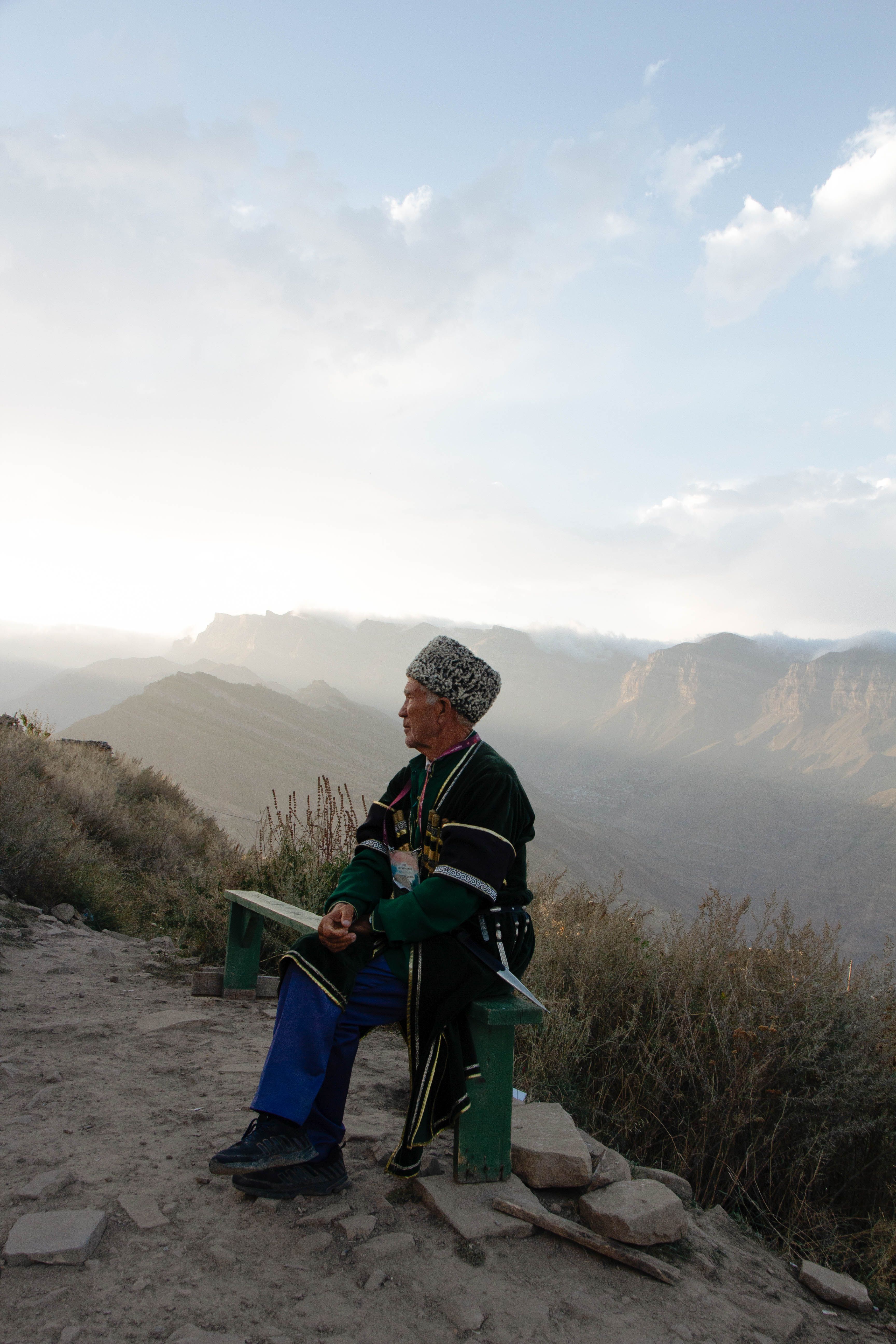 Smiling Man in Poncho Sitting and Posing in Mountains · Free Stock Photo