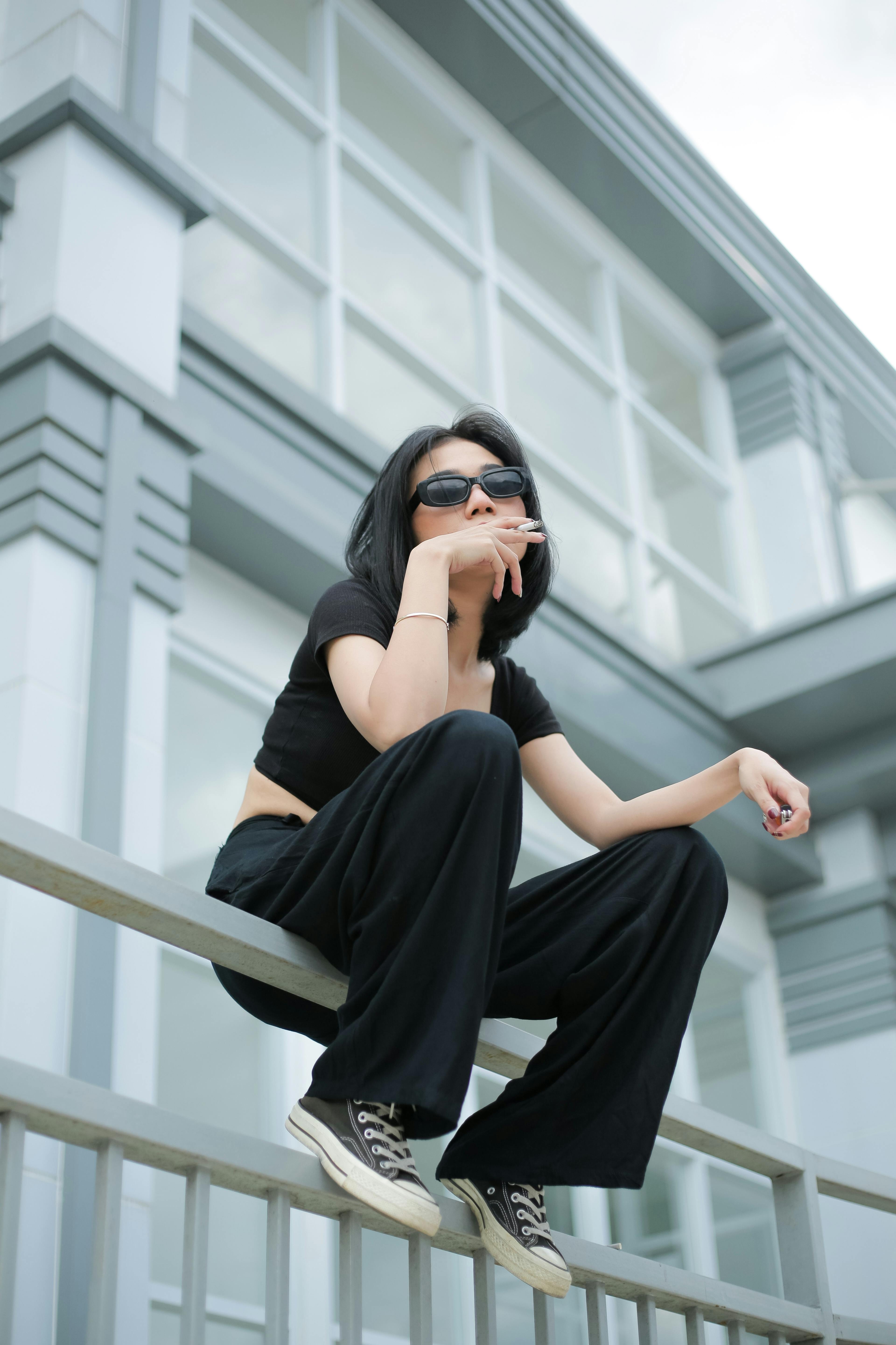 Woman with Sunglasses Sitting on Railing and Smoking Cigarette · Free ...